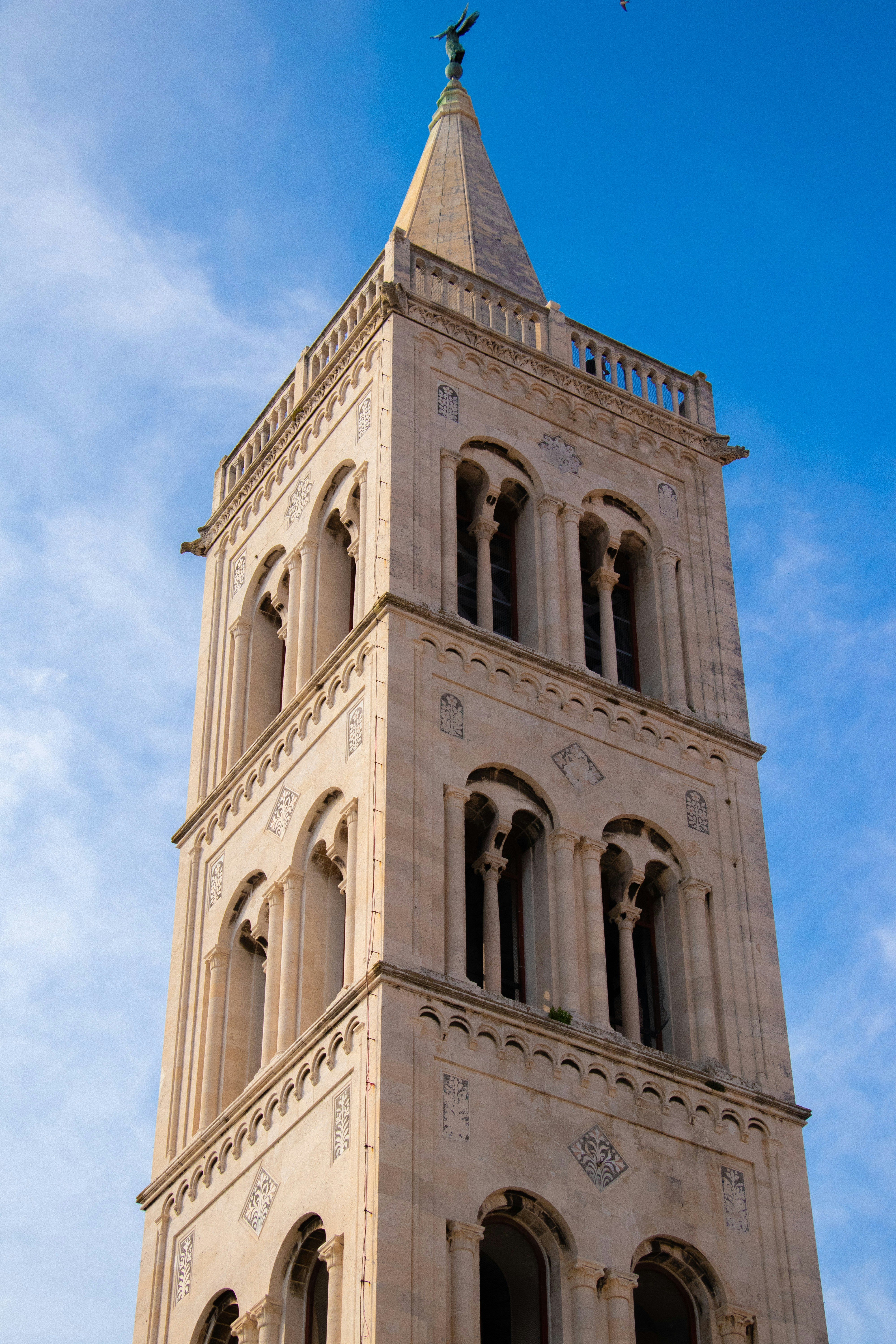 Historic bell tower rises against a clear blue sky, showcasing intricate architectural details and a statue atop. 