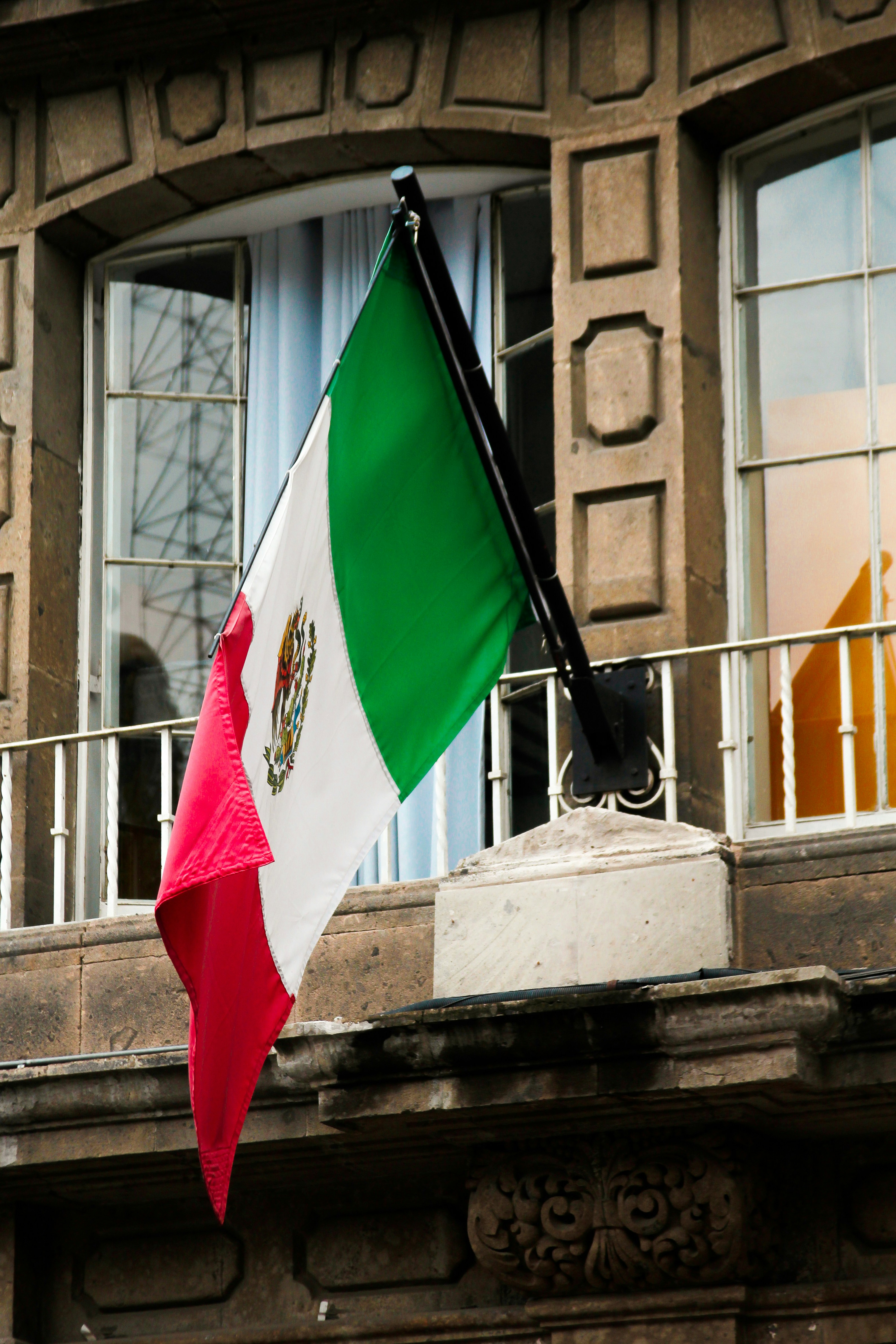 Flag of Mexico Draped Over a Weathered Balcony, Framed by Ornate Facades