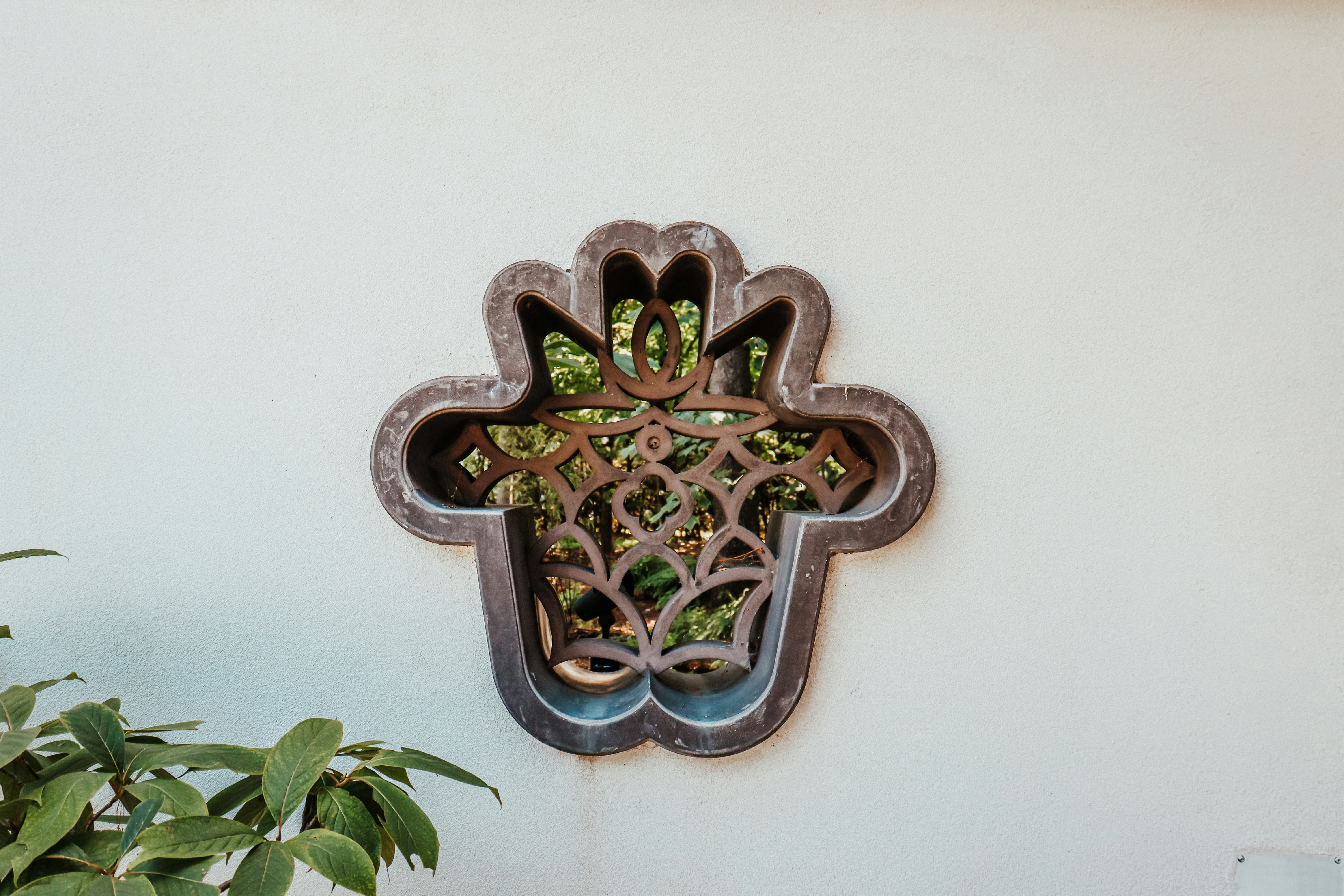 Hamsa's Veil: Ornate Metal Lattice on a Quiet White Wall