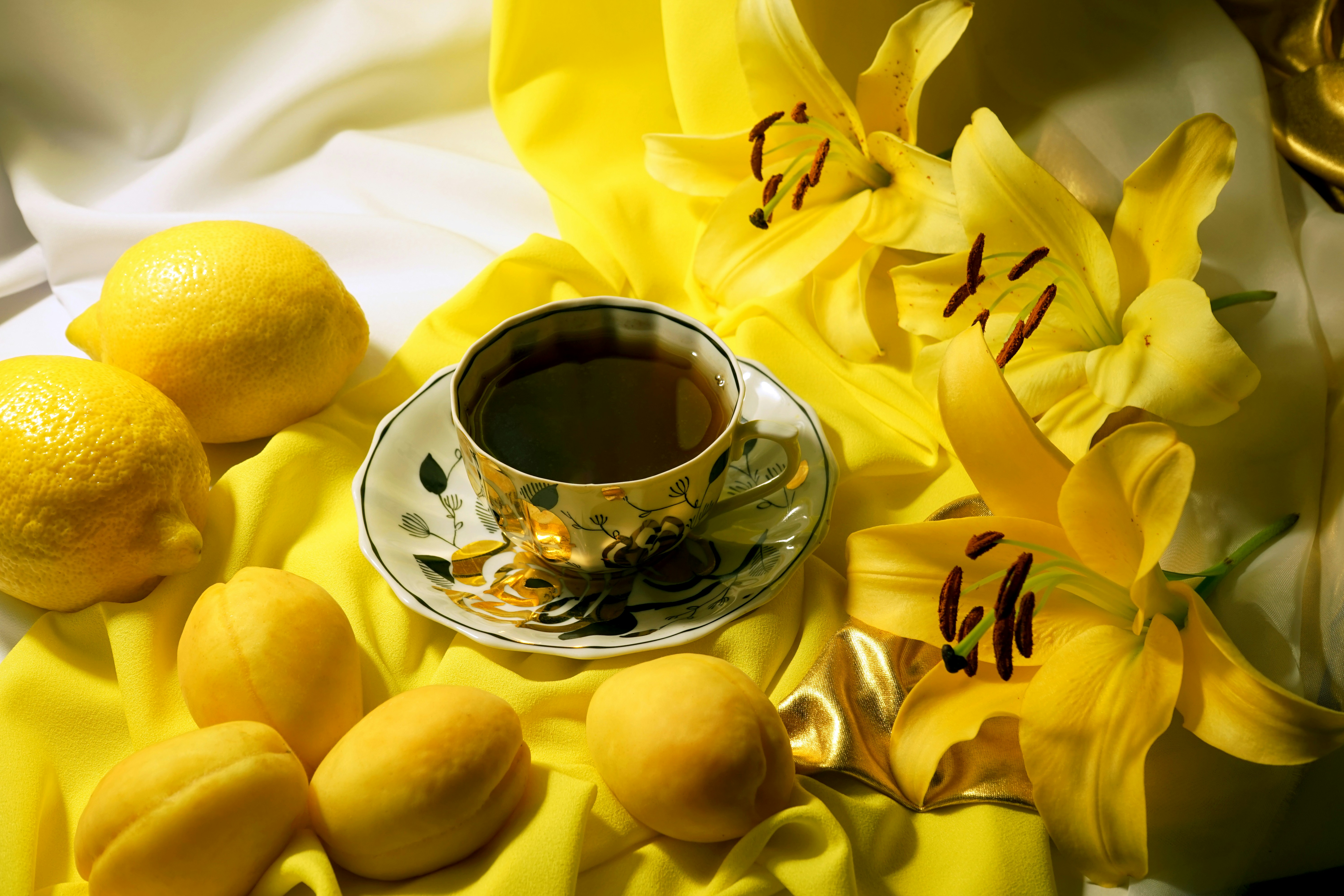 A cup of tea,ripe apricots, ripe lemons and yellow lilies-close-up on a decorative background made of fabrics.