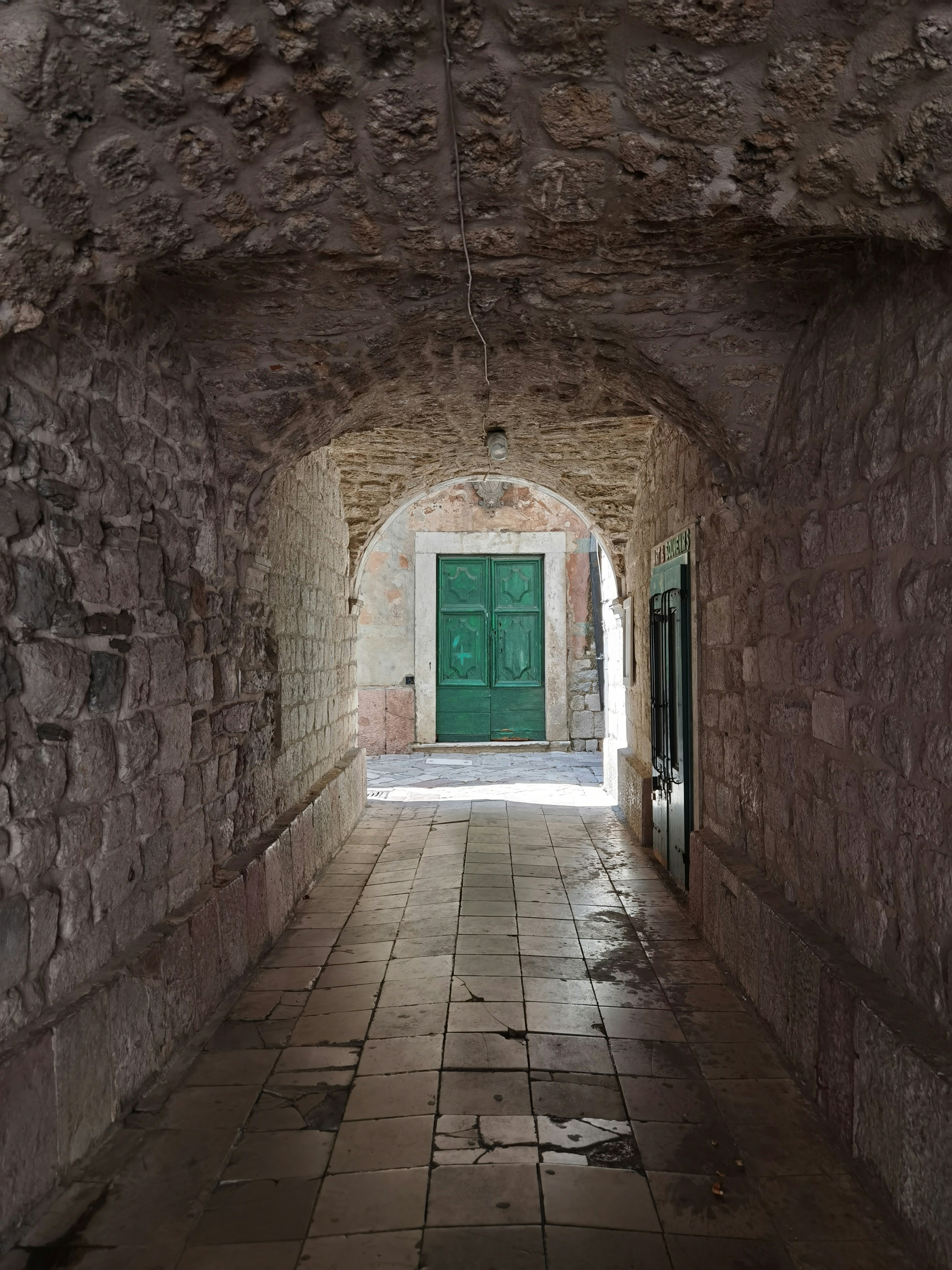 Stone archway leading to a vibrant green door at the end of a narrow corridor, illuminated by soft overhead light.