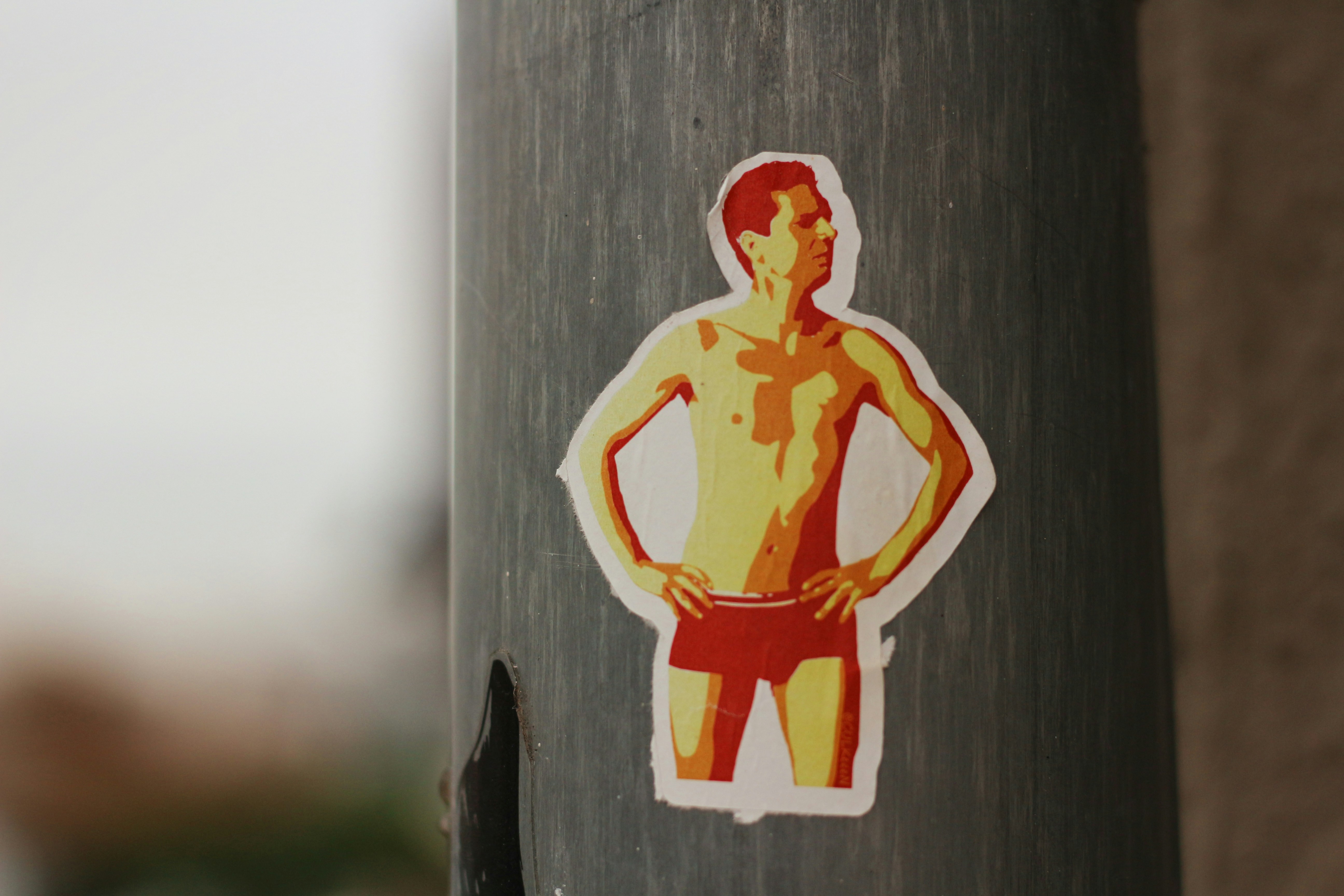 Stickered Stature: Orange figure on a weathered post