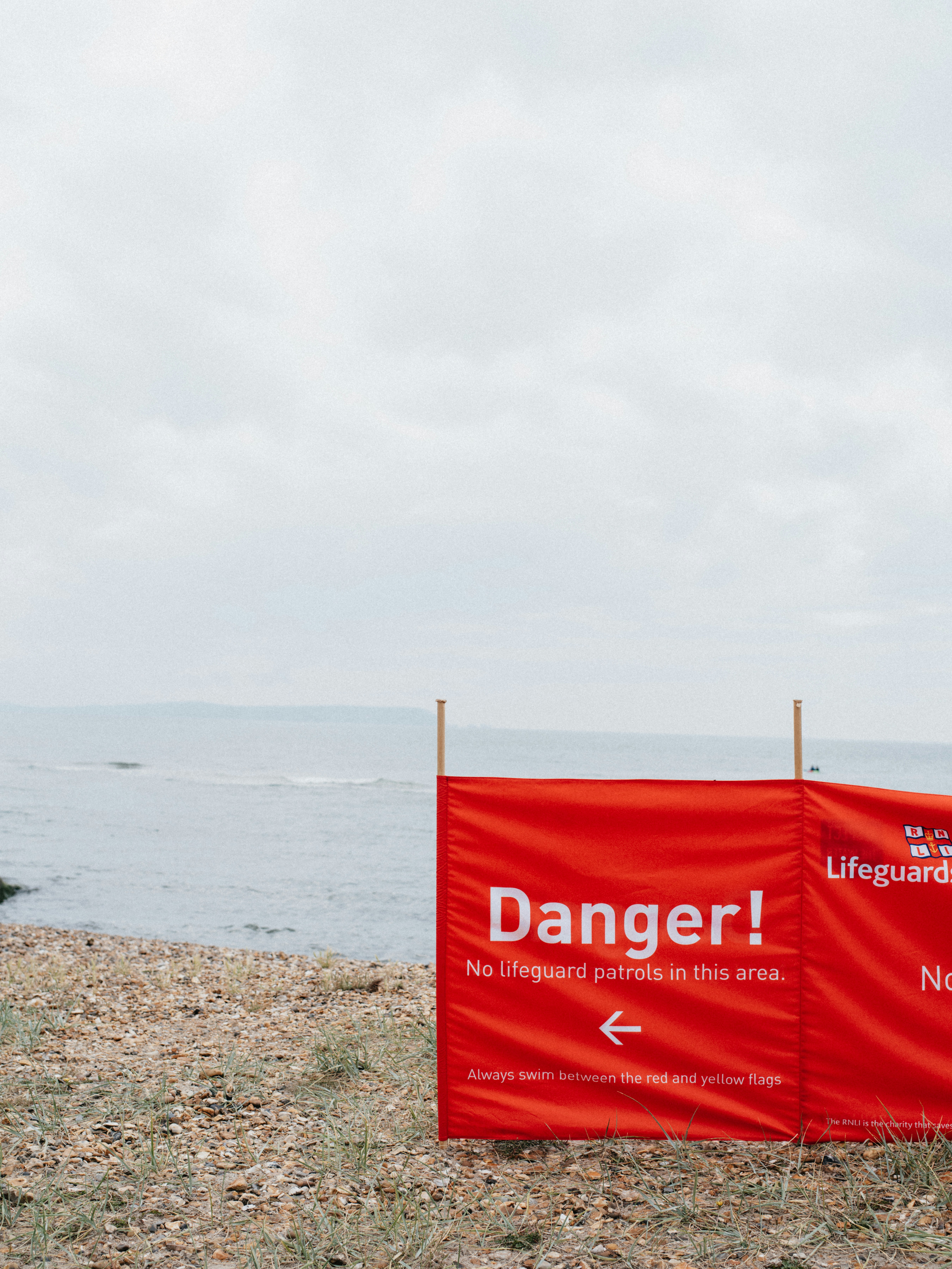 Red Danger Banner on a Pebble Beach Declares No Lifeguard Patrols