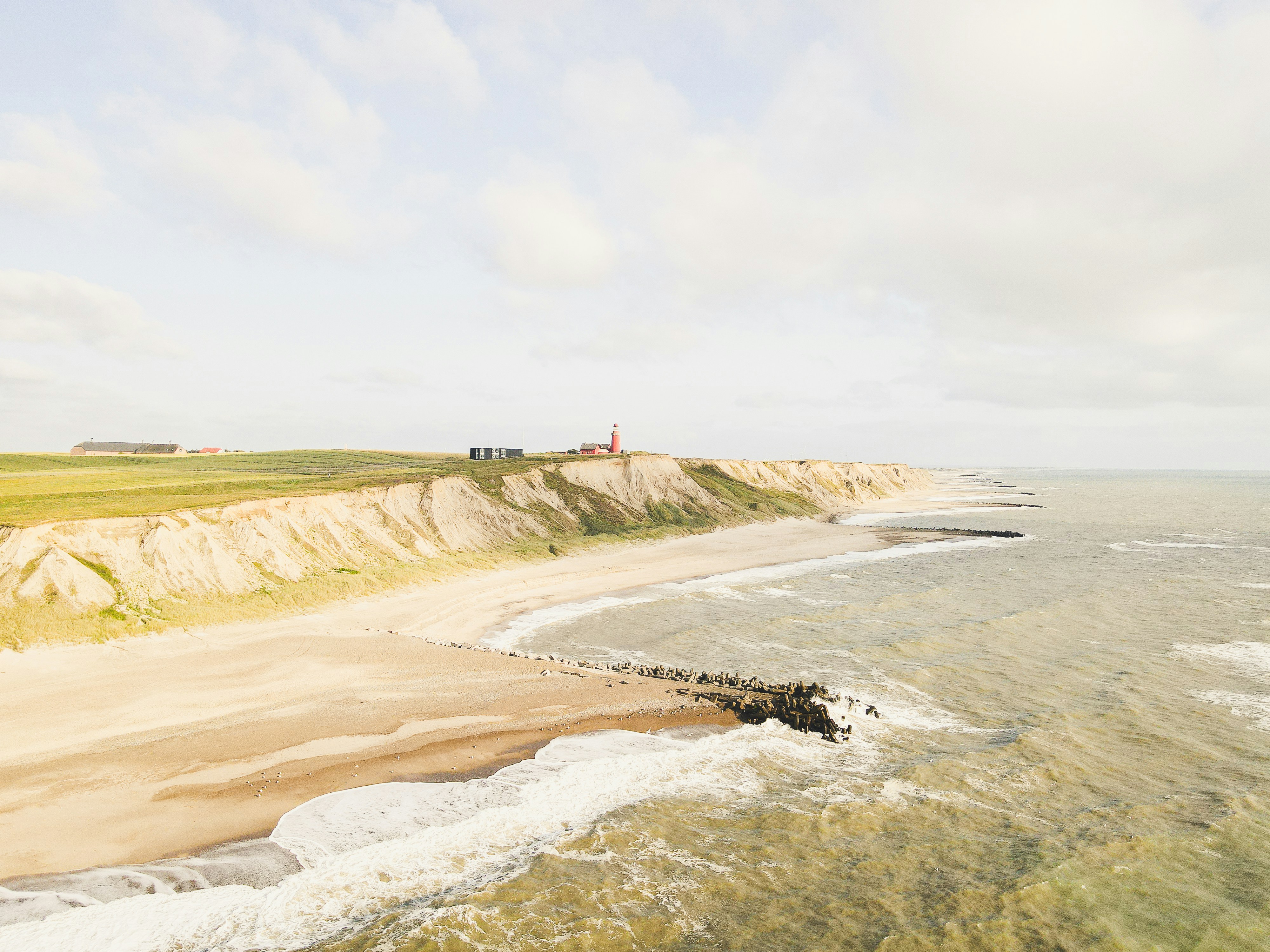 A sweeping coastal landscape featuring dramatic cliffs, gentle waves, and a distant lighthouse, illustrating the harmony between land and water.
