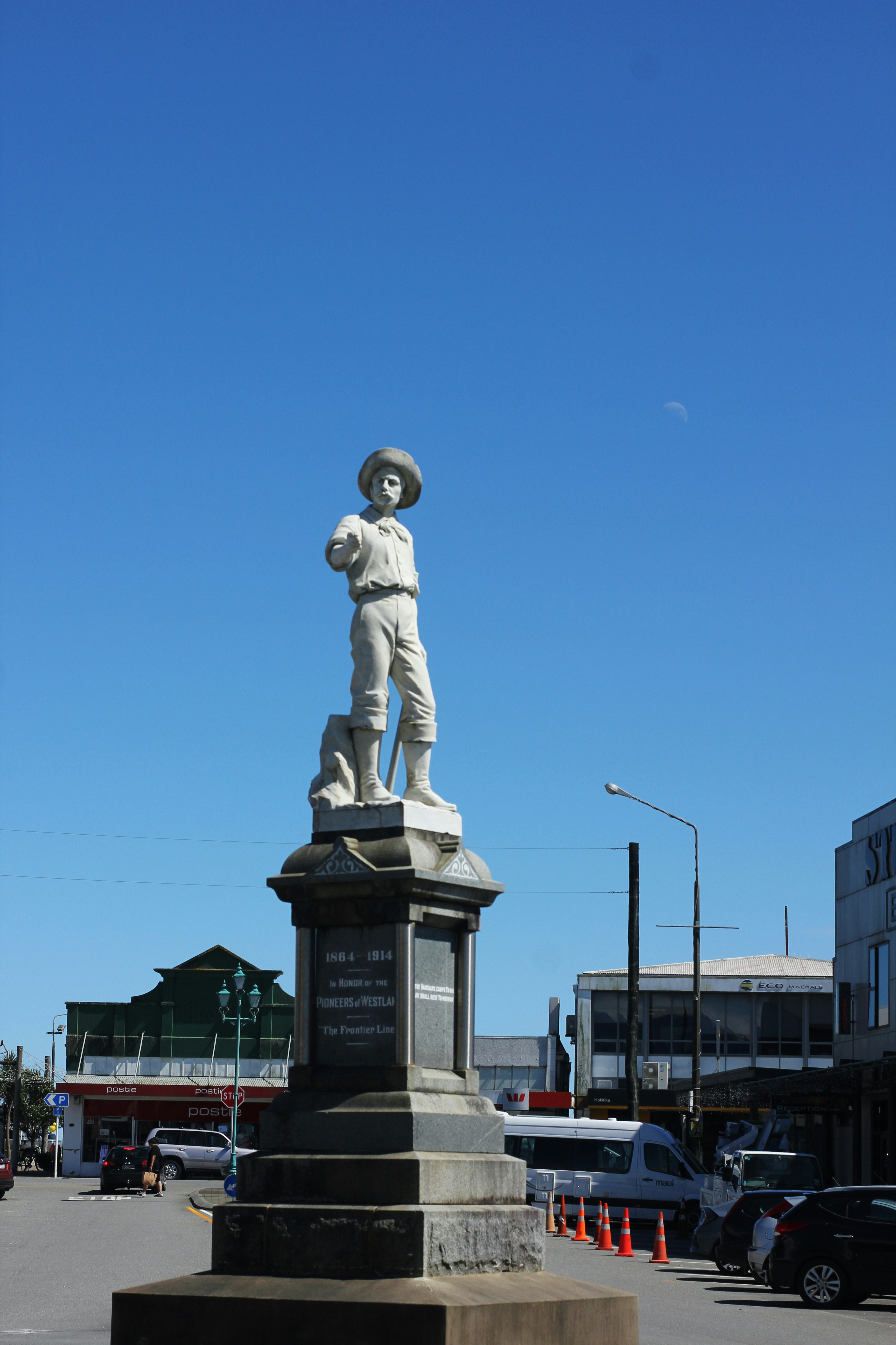Statue commemorating a historical figure, standing tall against a clear blue sky, surrounded by urban life.
