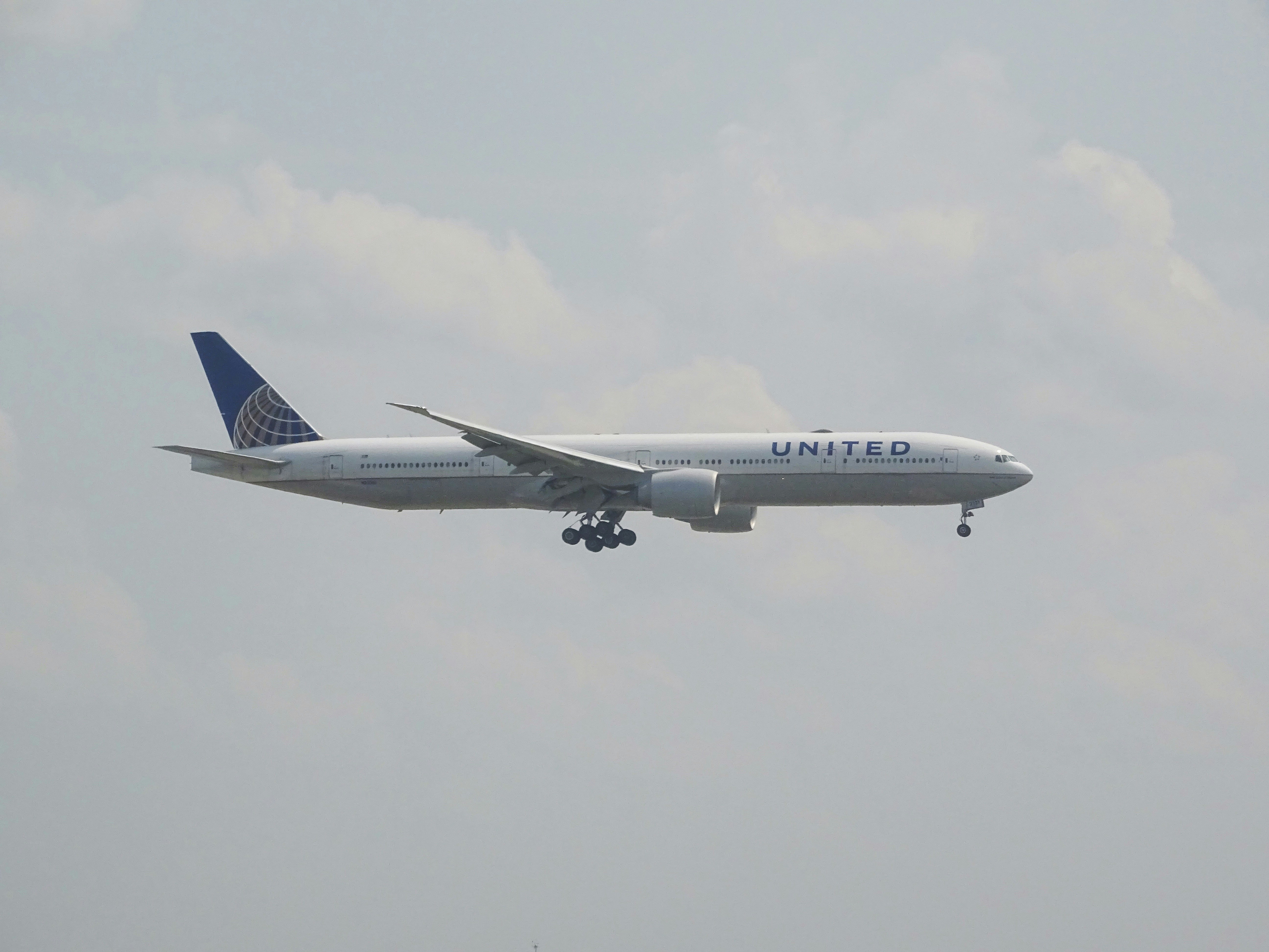 United Airlines jet in landing approach, captured in a photograph with landing gear extended against a cloudy sky.
