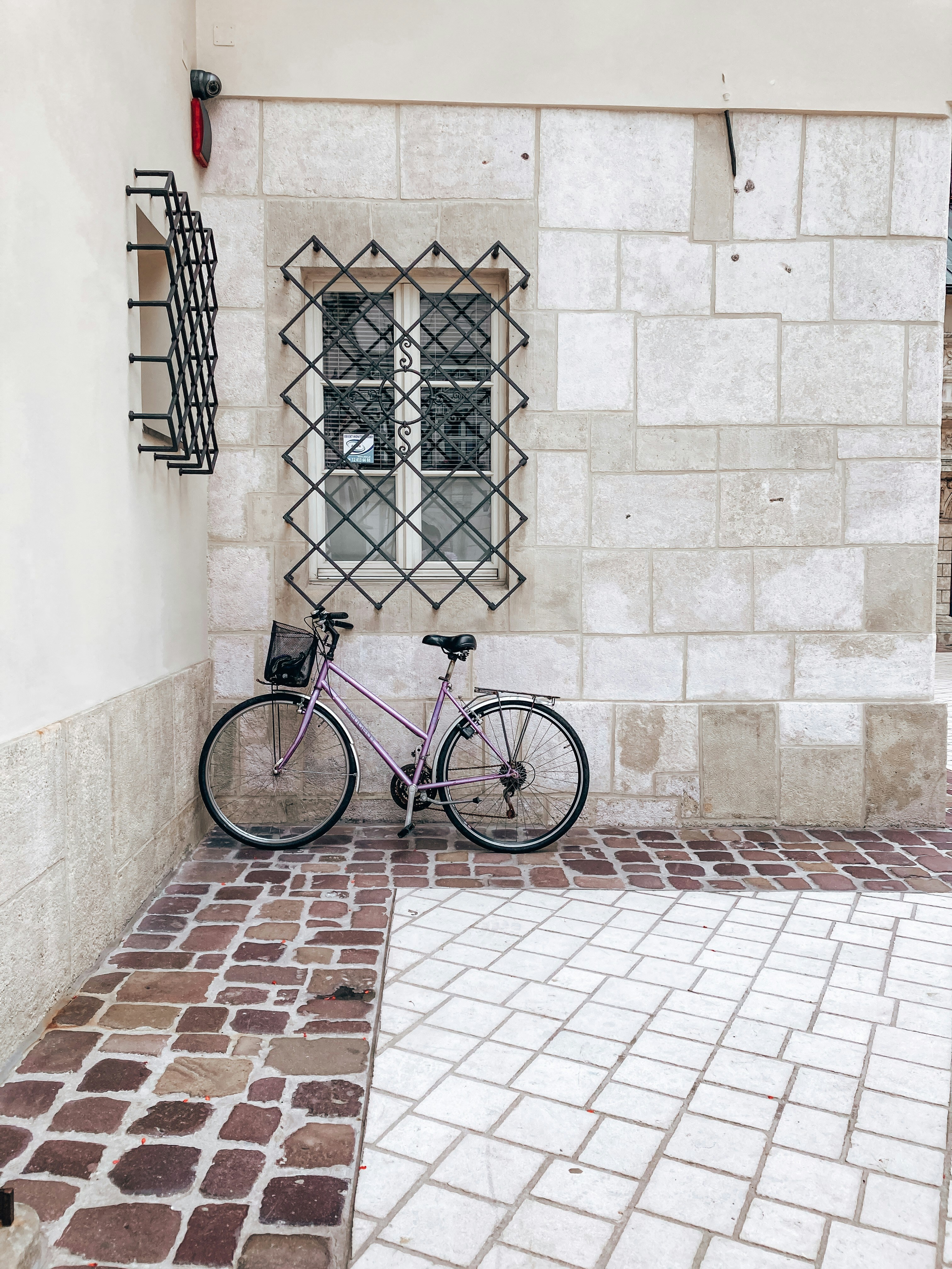 Lilac Bicycle Leaning Against a Diamond-Pattern Window in a Stone Courtyard