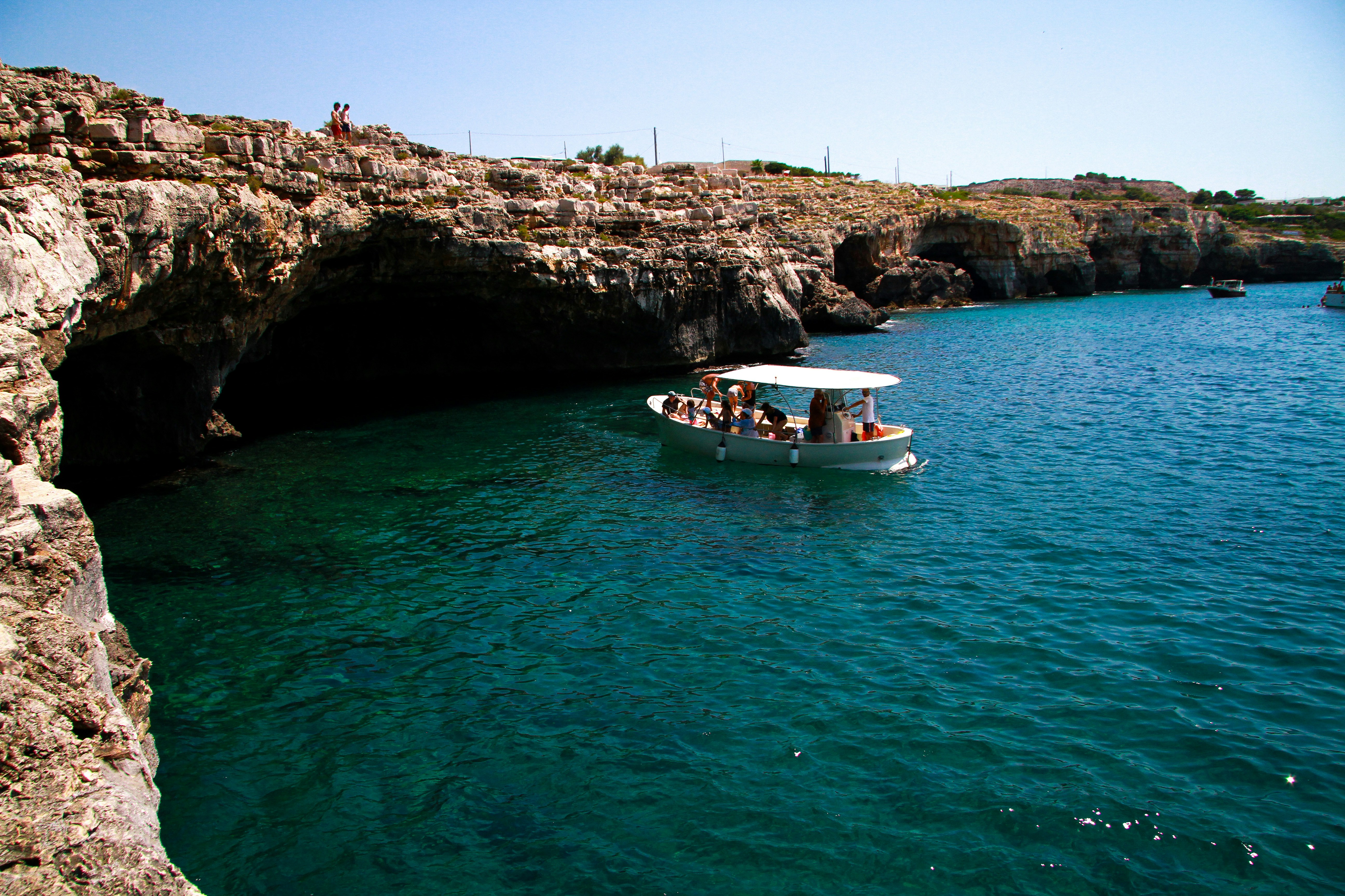 Small boat navigates a serene cove with rocky cliffs and clear blue water under a bright sky.