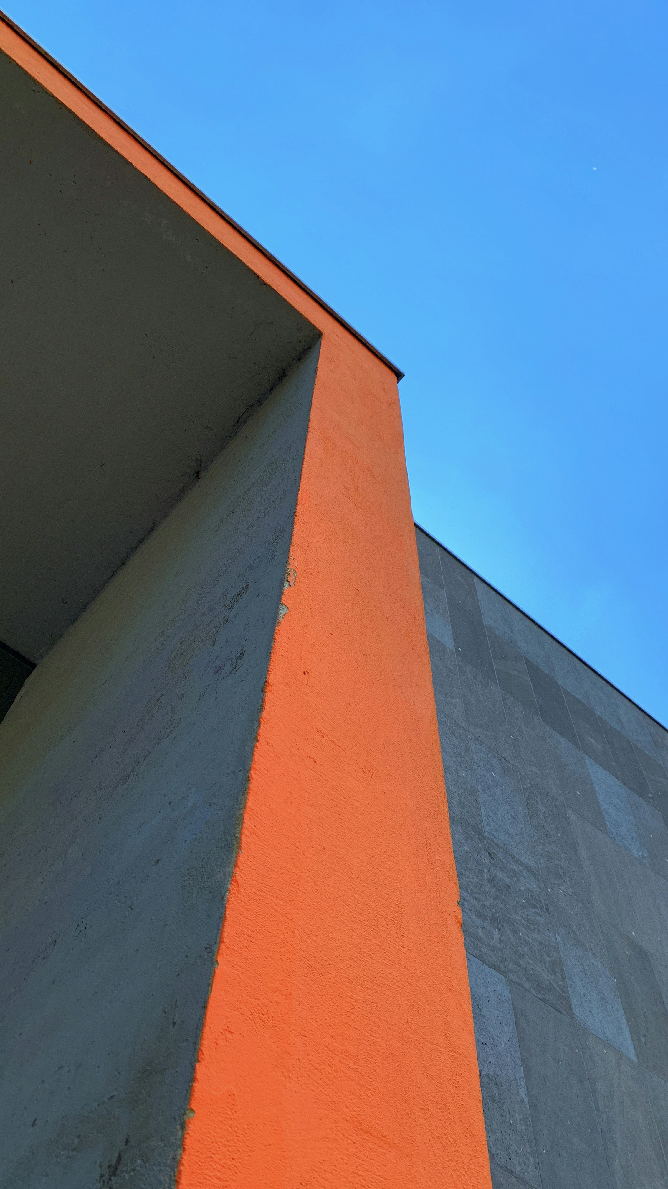 Orange Vertical Edge Carves the Modern Facade Against a Clear Blue Sky