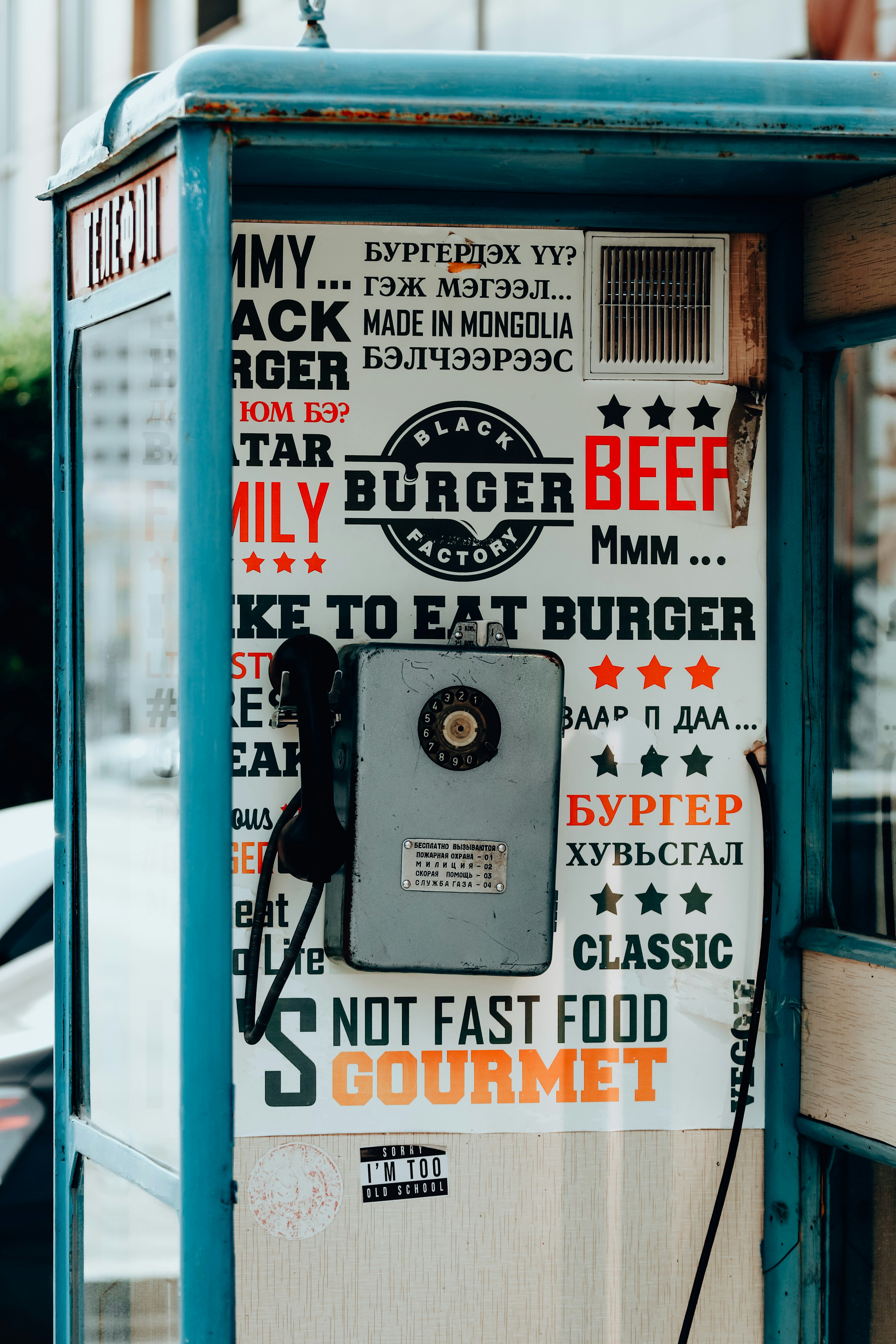 Blue Kiosk Collage: Multilingual Burger Ads on a Weathered Facade