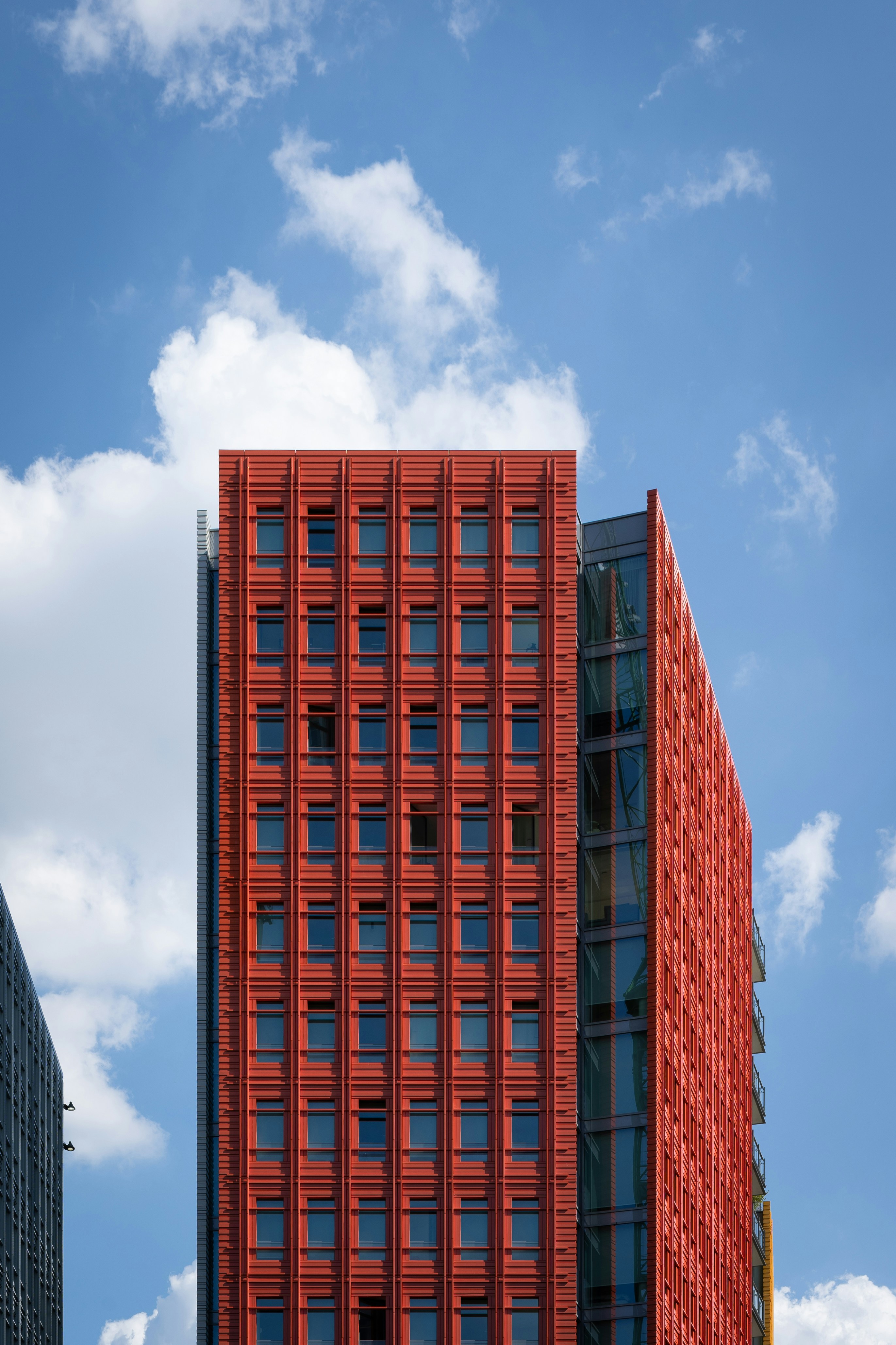 A striking red building facade contrasted against a bright blue sky with fluffy clouds, showcasing modern architectural design.
