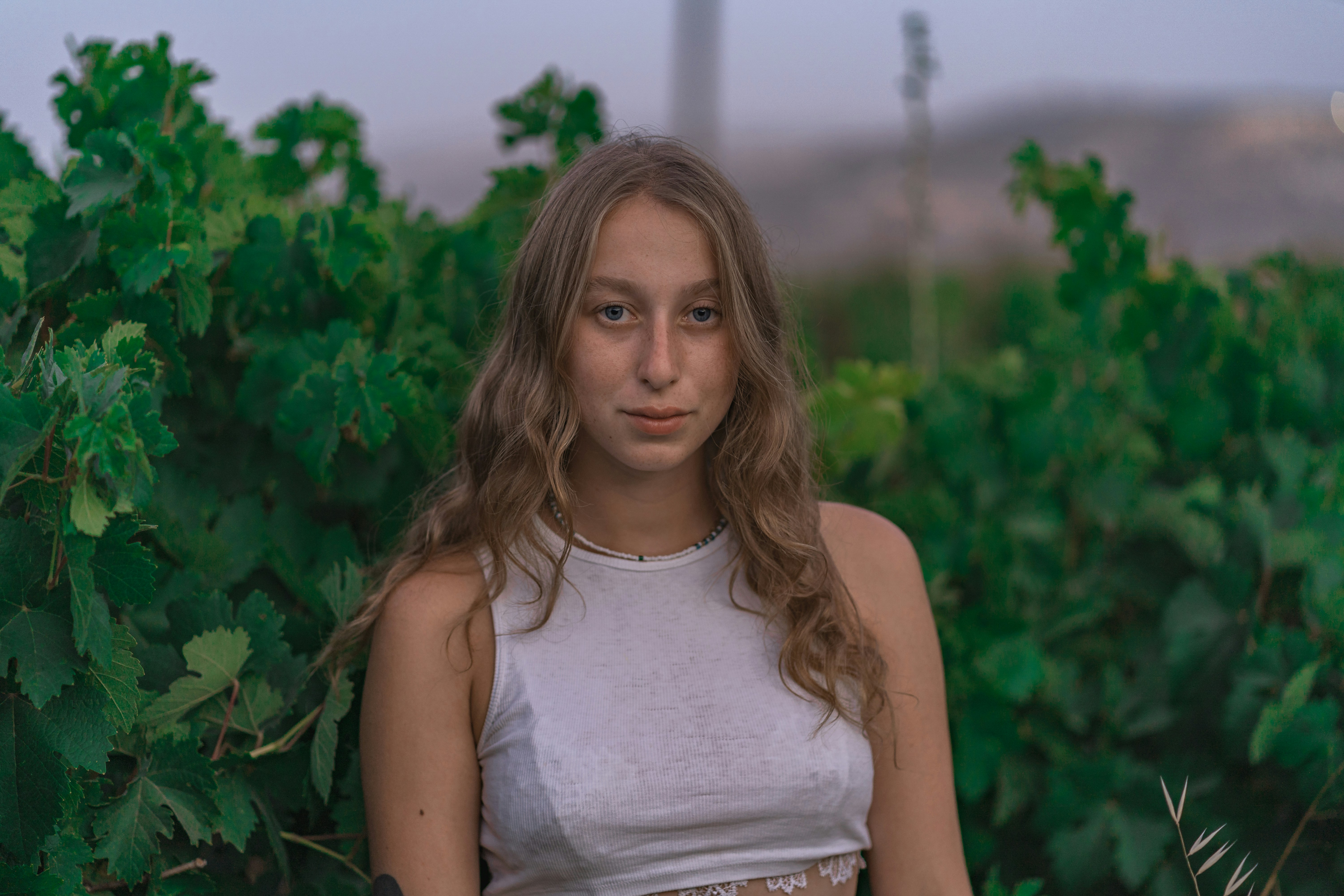 woman in white tank top standing beside green plants during daytime