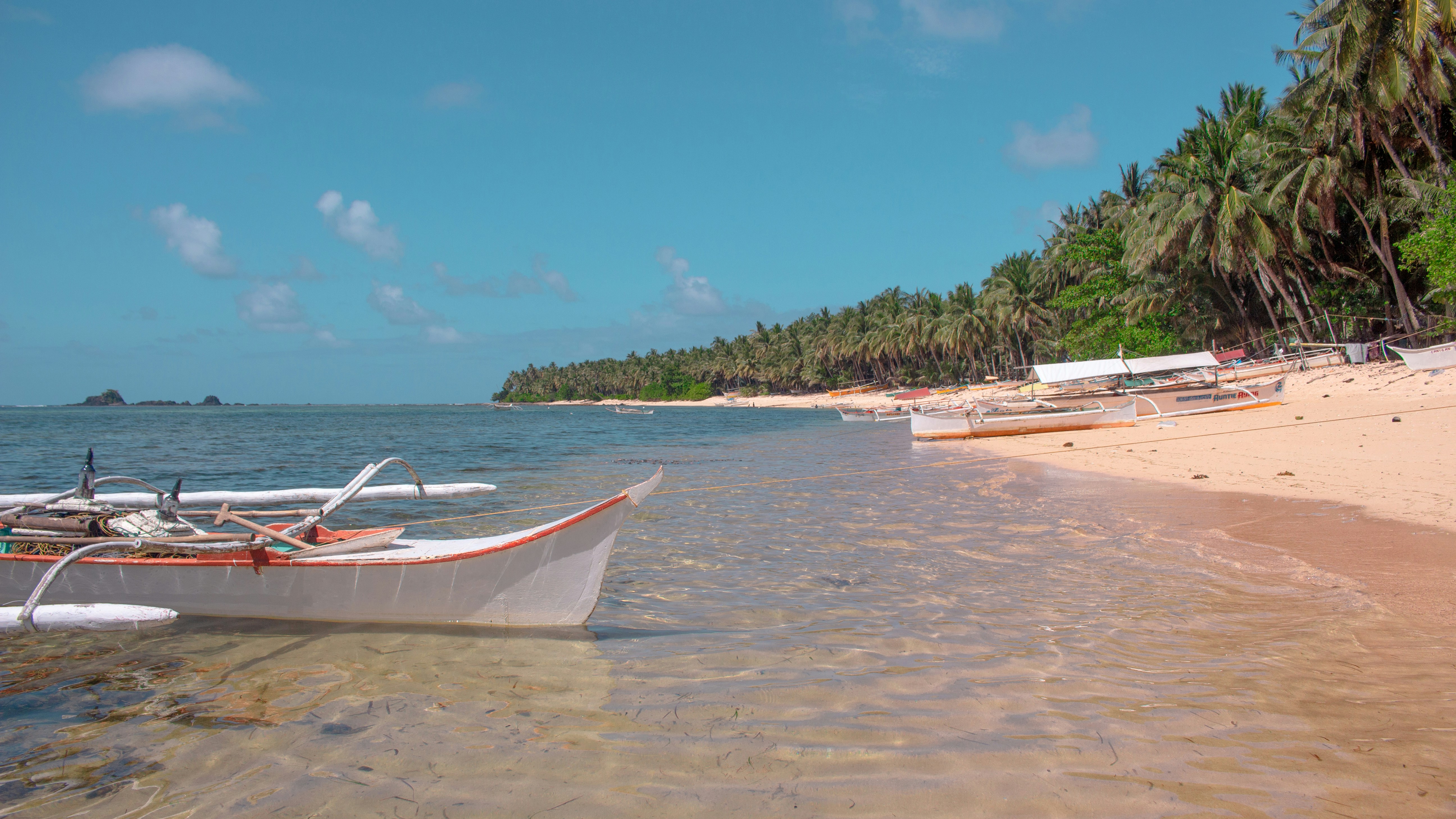 White and red boat rests on a sandy beach under a clear blue sky.