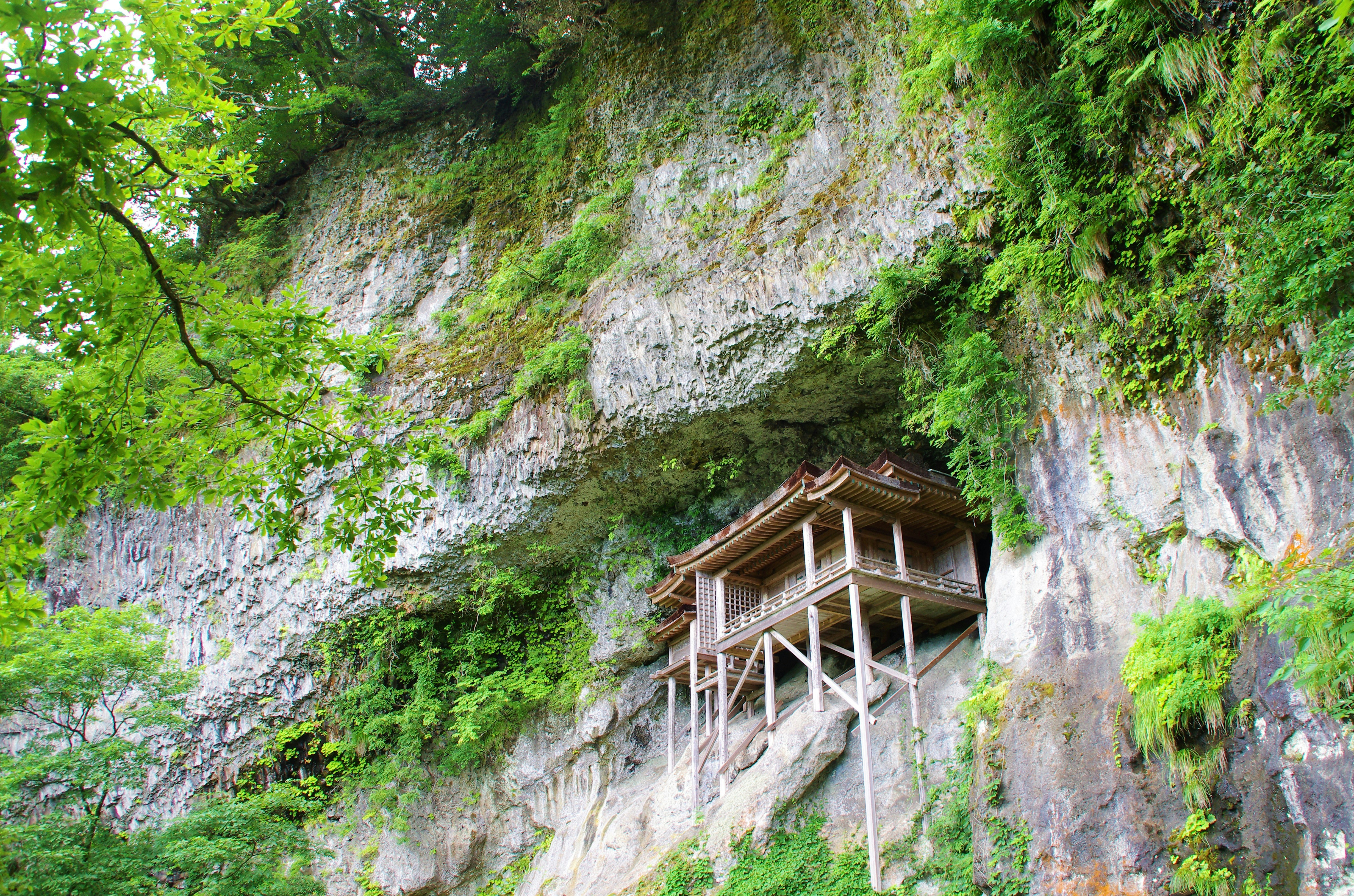Traditional wooden structure perched on a rocky cliff, surrounded by lush greenery and steep stone formations.
