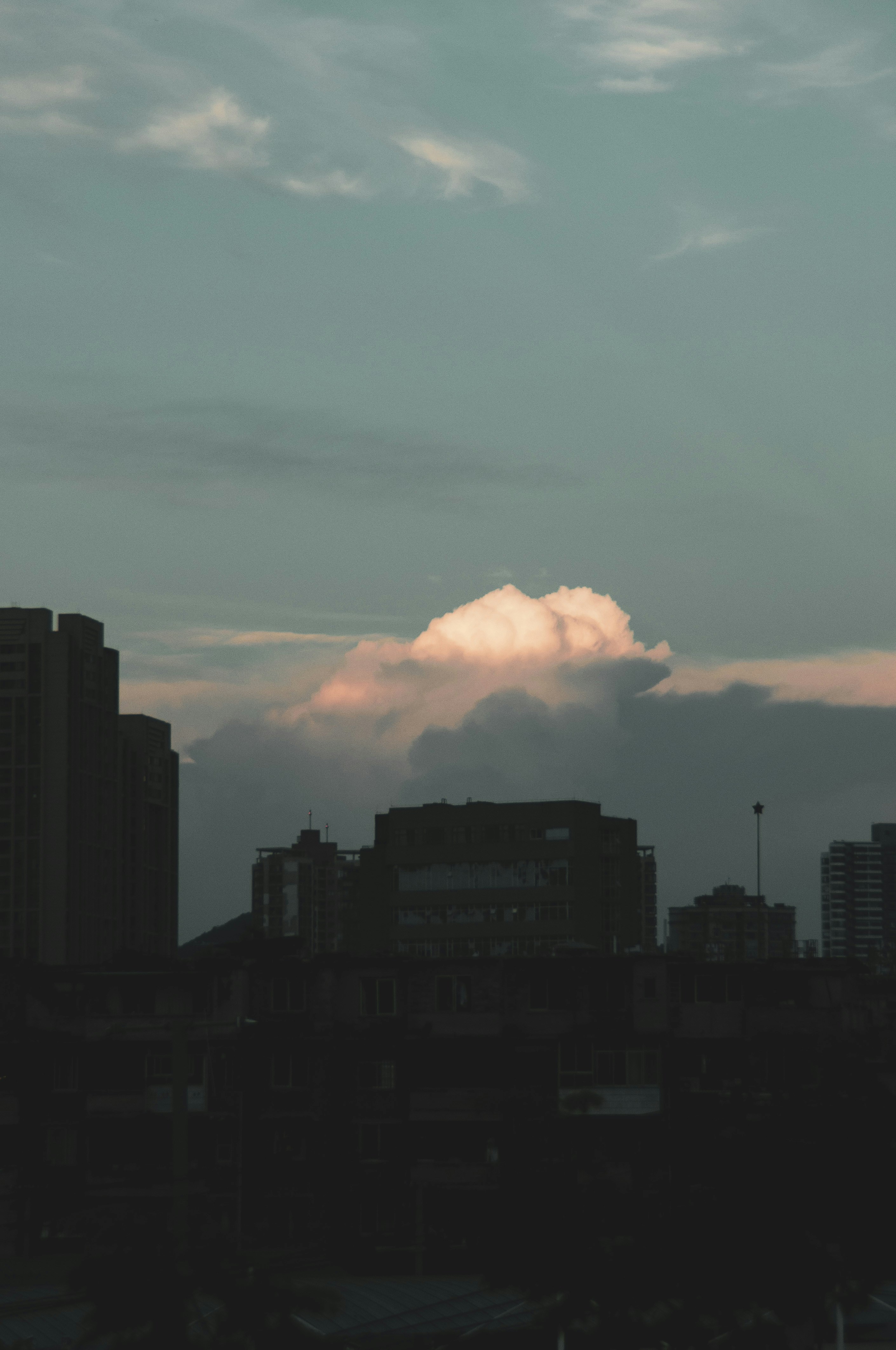 A soft, illuminated cloud looms above a city skyline, contrasting against the darkening buildings below.
