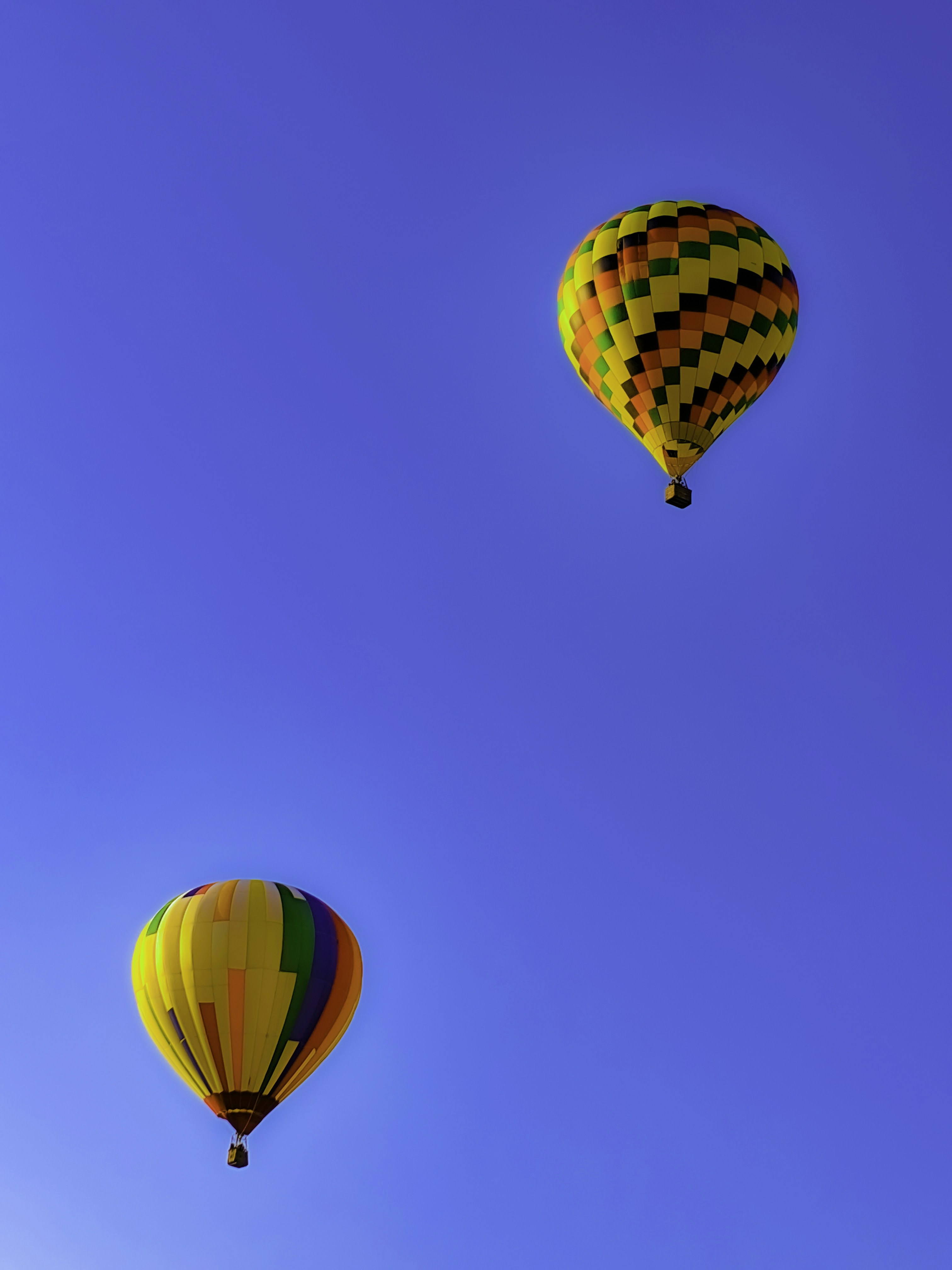 Two vibrant hot air balloons soaring against a clear blue sky, showcasing their colorful patterns and the freedom of flight.