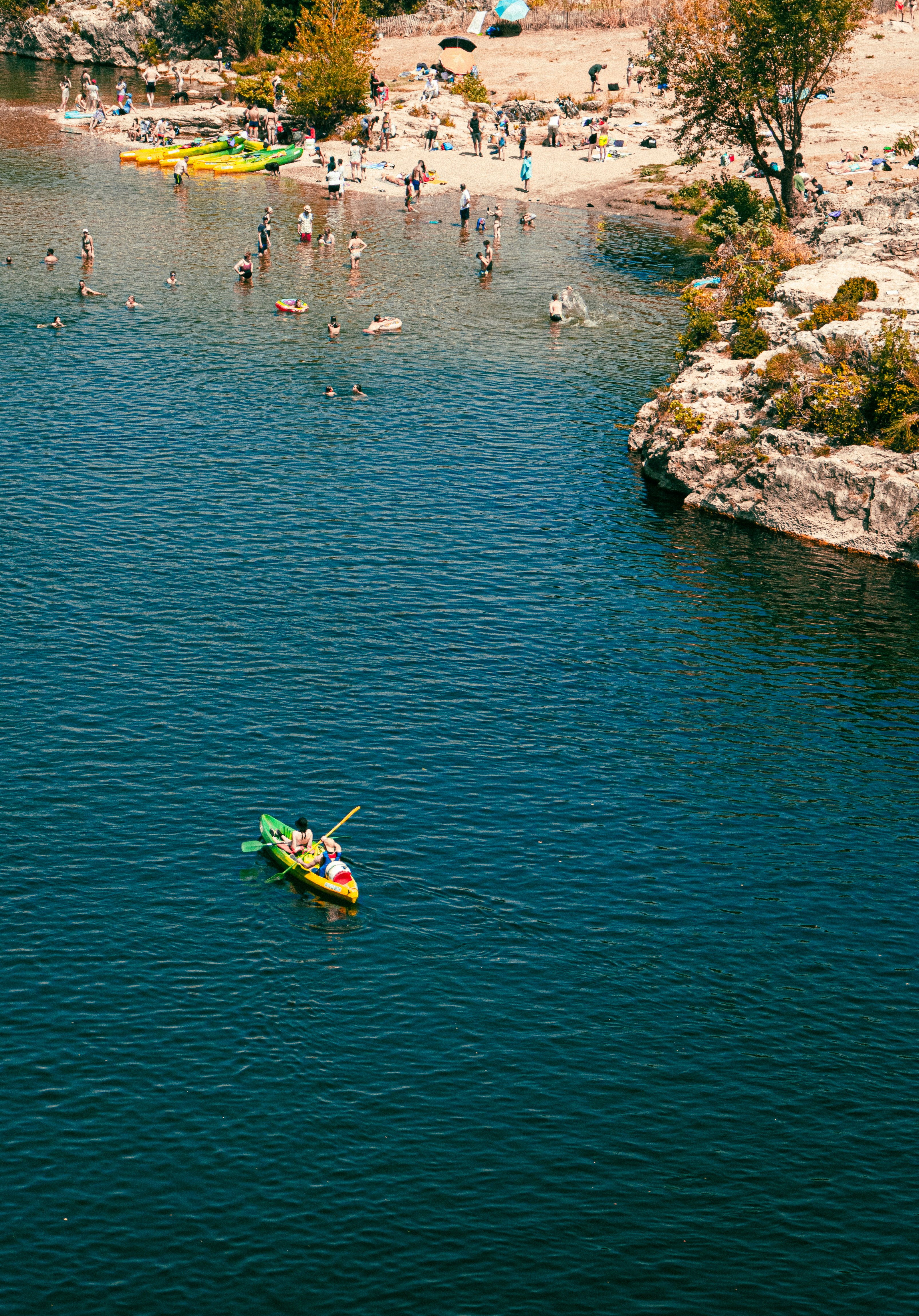 Emerald Kayak Gliding Past a Lively Riverside Beach