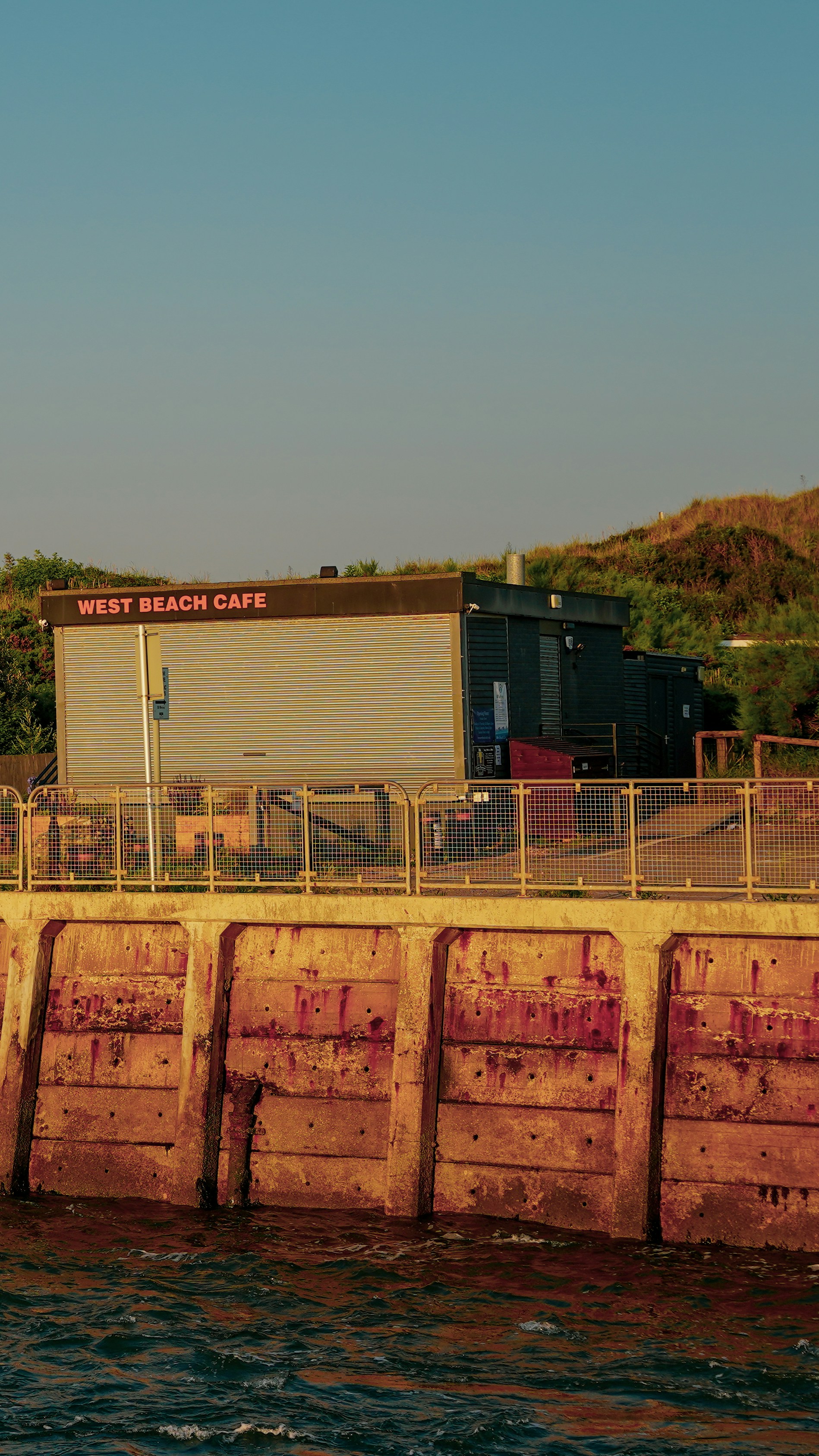West Beach Cafe nestled alongside a weathered seawall, with gentle waves lapping at the shore. The scene captures a tranquil coastal ambiance.
