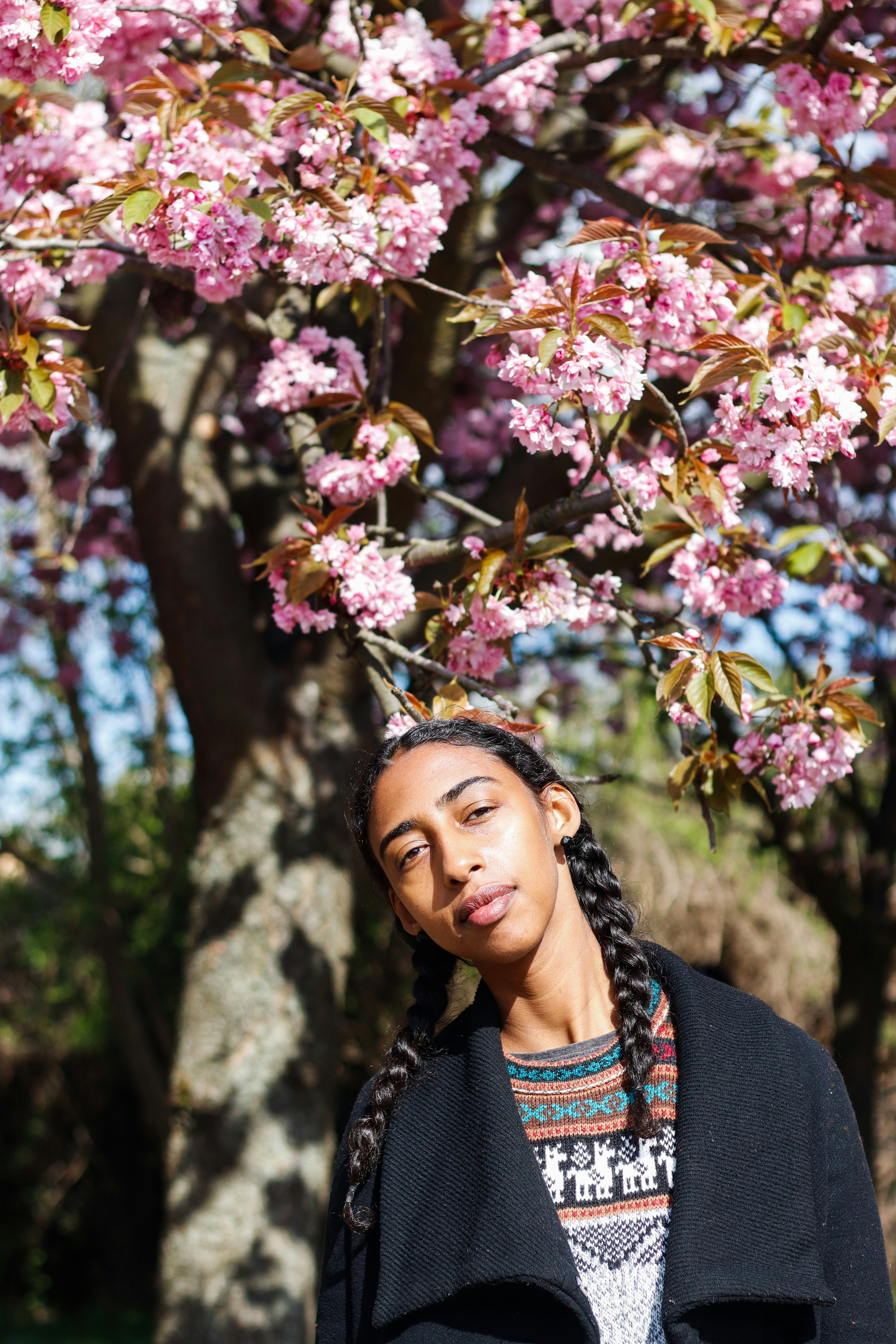 A young woman stands under a blooming cherry tree, framed by vibrant pink flowers, showcasing her unique style and serene expression.