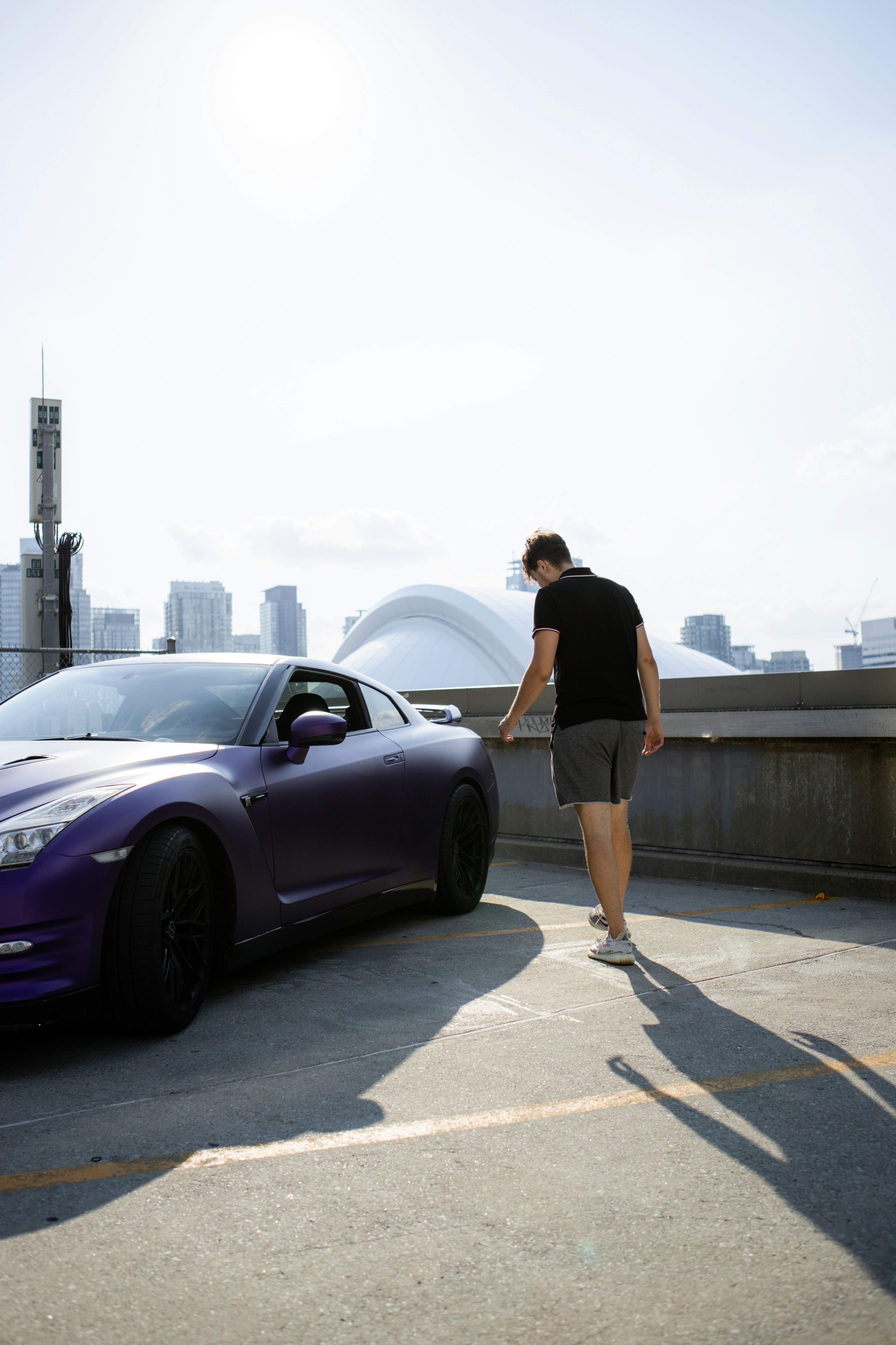 Person standing beside a purple sports car on a rooftop with a city skyline in the background.