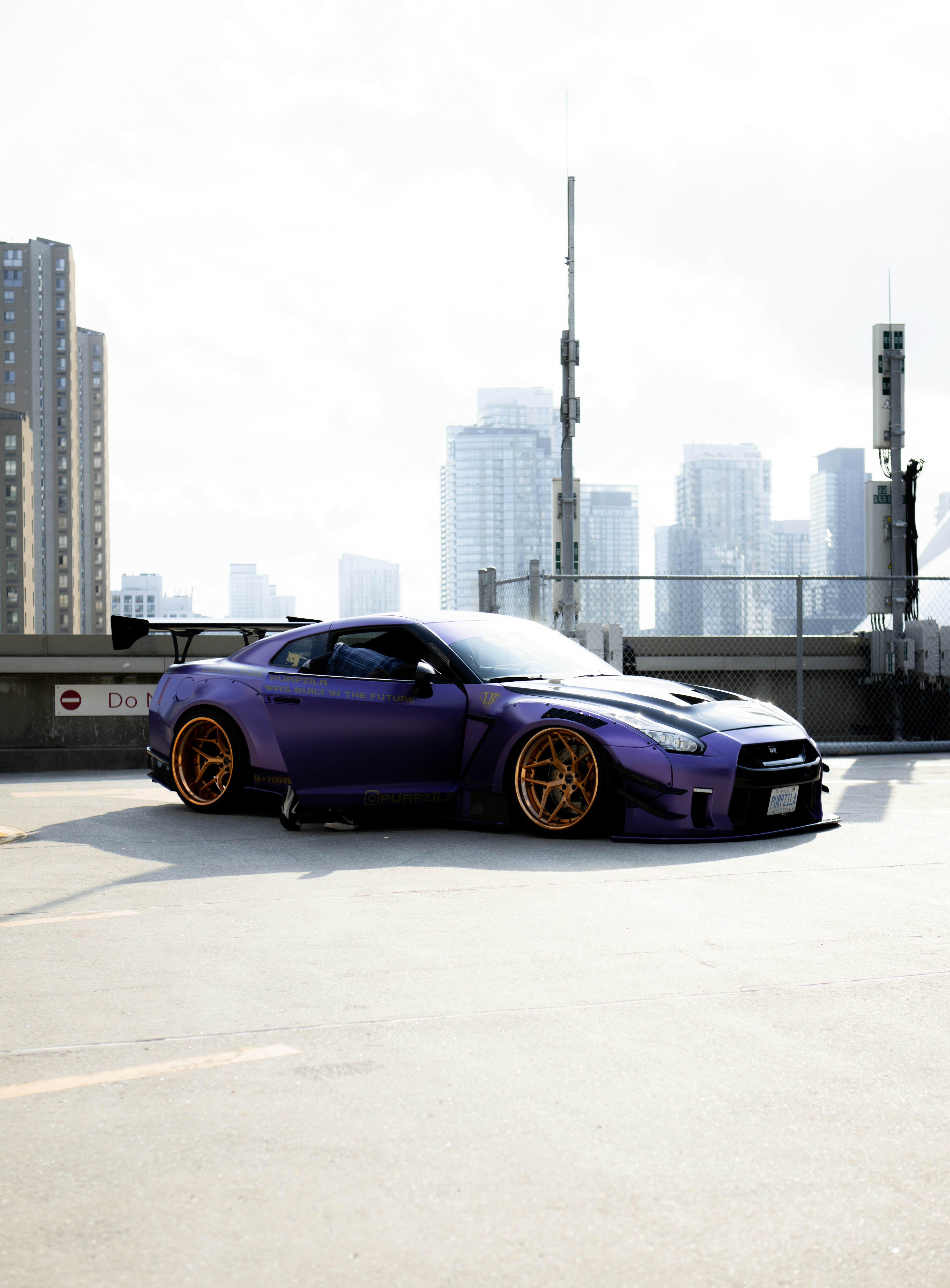 Modified purple sports car with striking orange wheels parked on a rooftop against a city skyline.