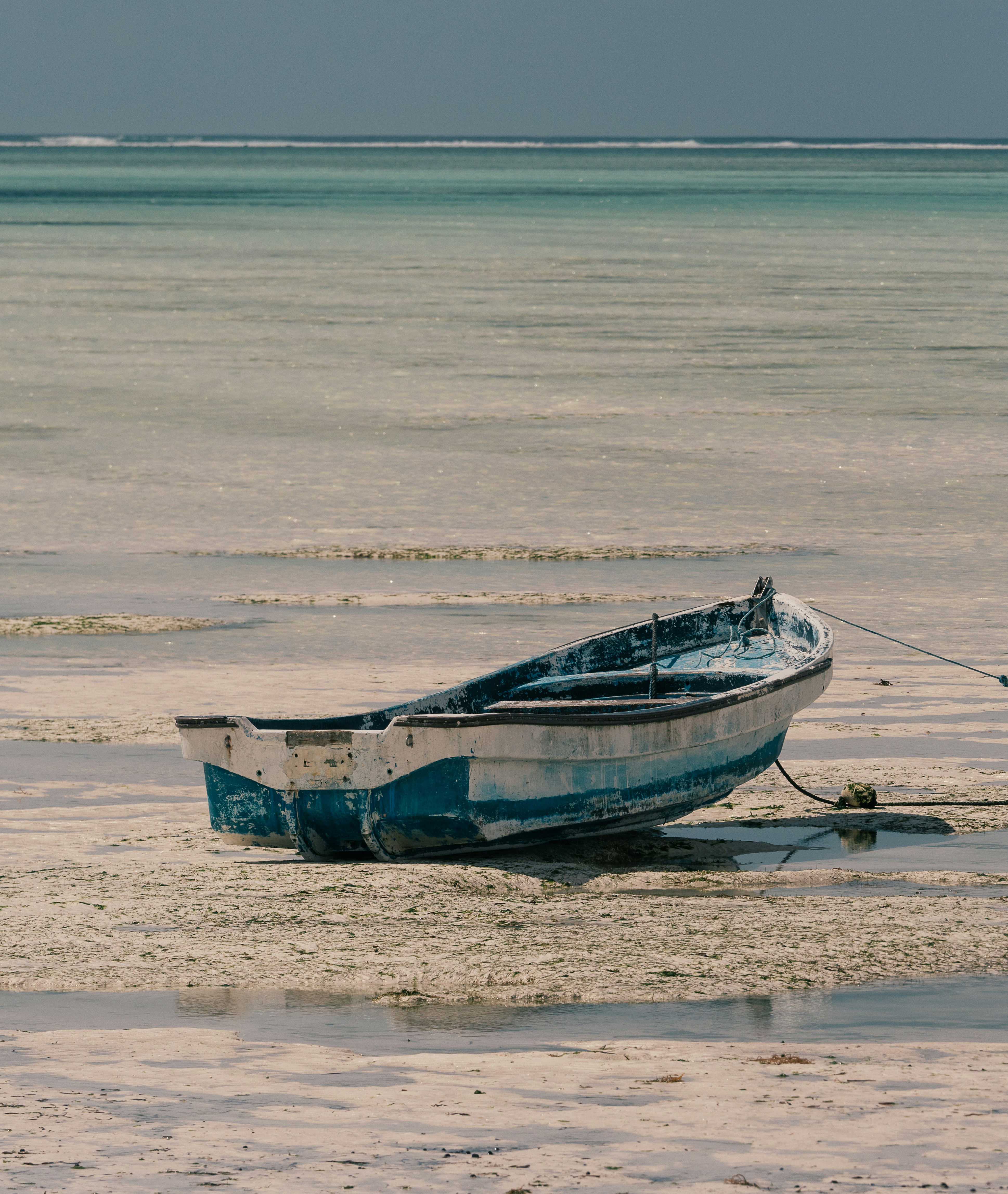 A weathered boat rests on a shallow shore, surrounded by a serene expanse of water and sand. The scene captures the tranquility of low tide.