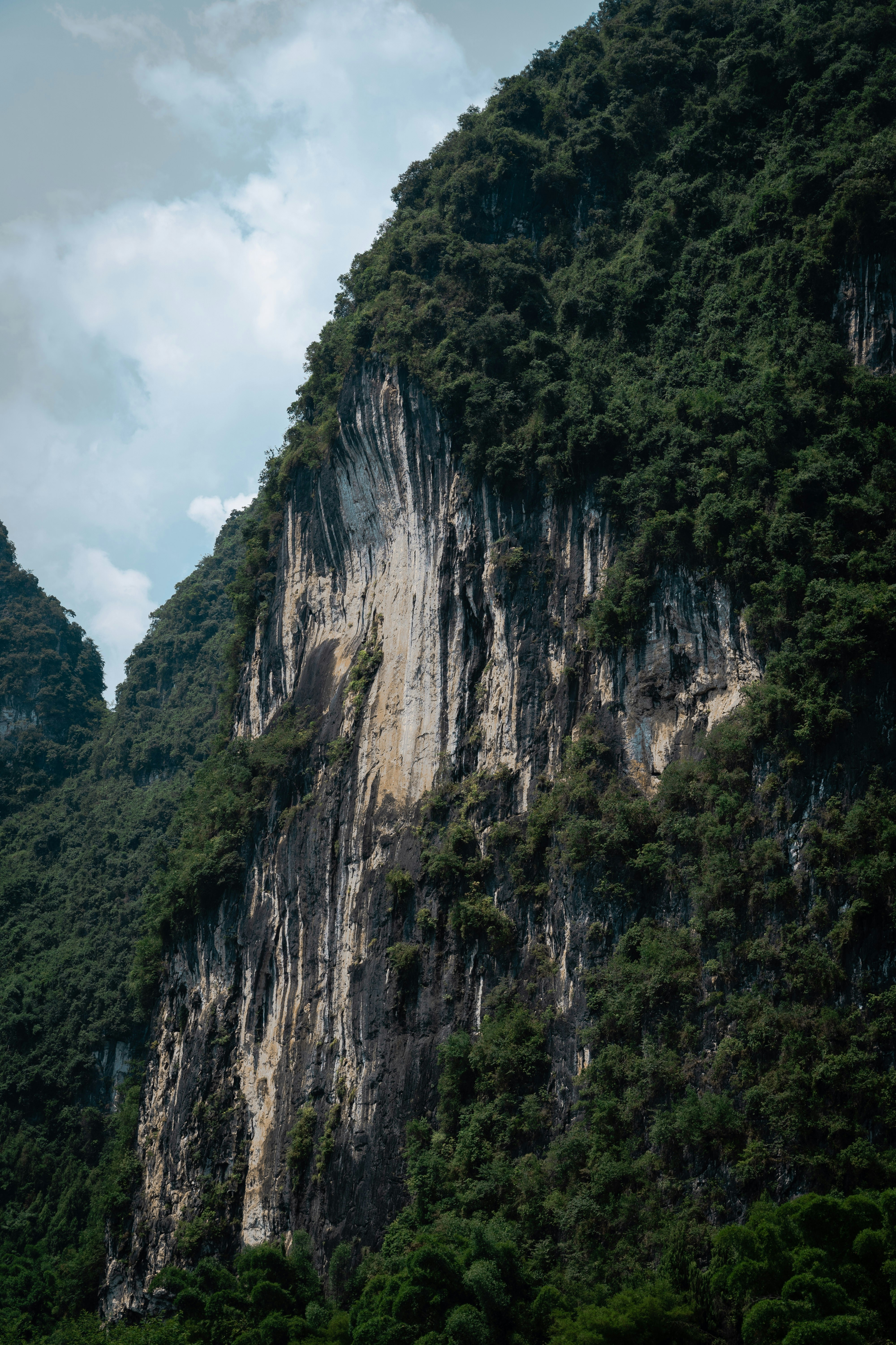 Steep, forested cliffs rise dramatically against a cloudy sky.