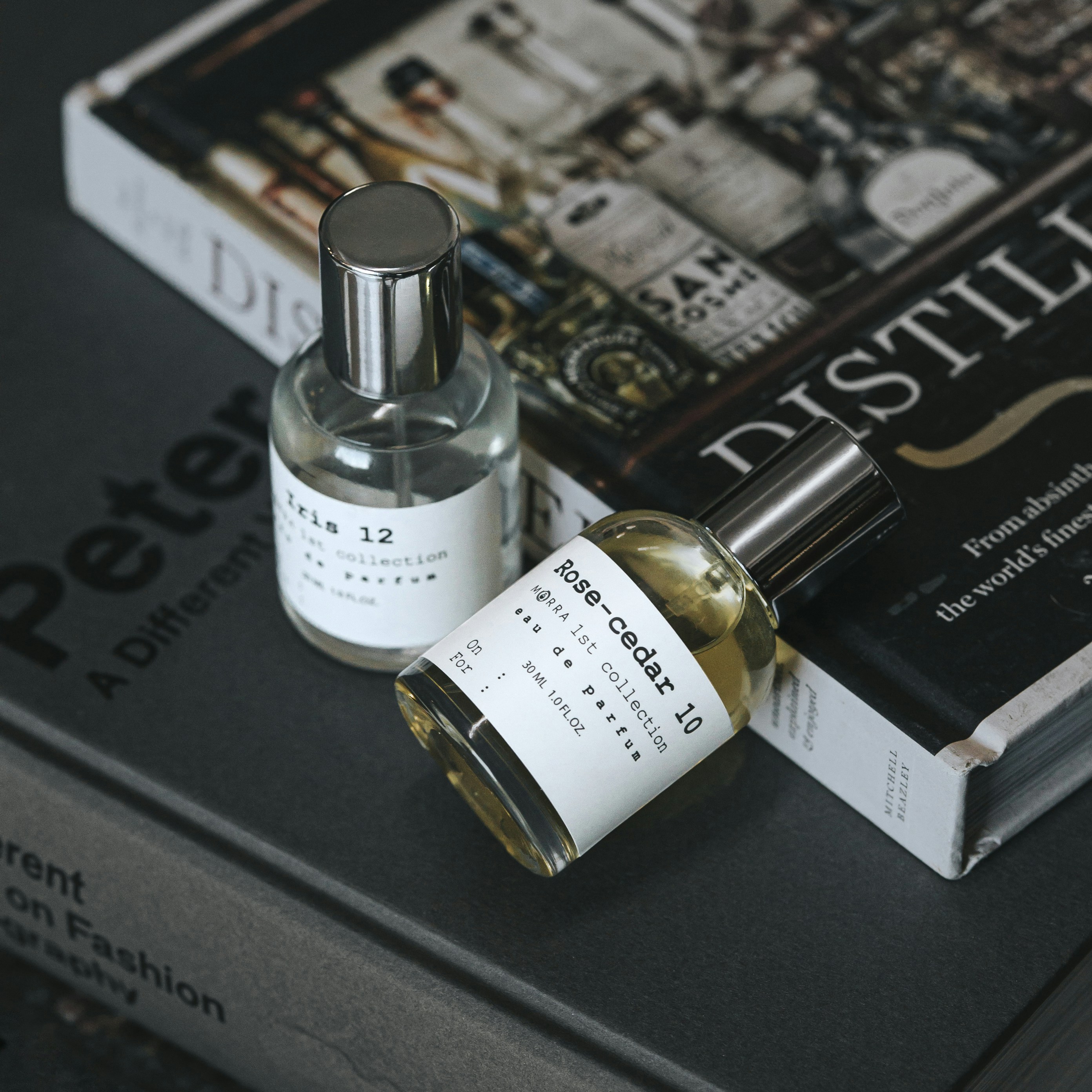 Two elegantly designed perfume bottles, labeled 'Iris 12' and 'Rose-Cedar 10', placed atop a stylish book with vintage aesthetics.