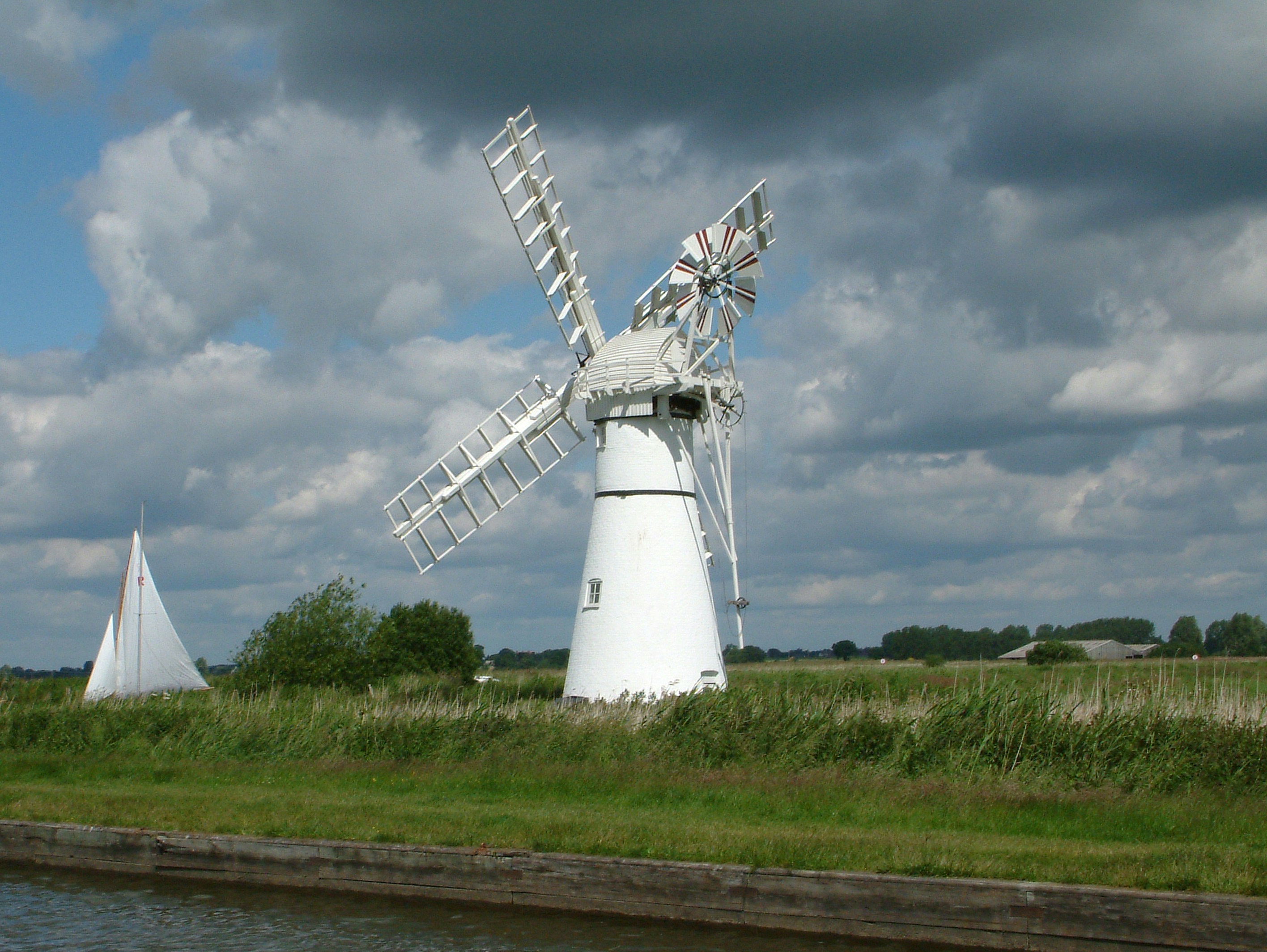 White windmill standing beside a tranquil waterway under a cloudy sky.