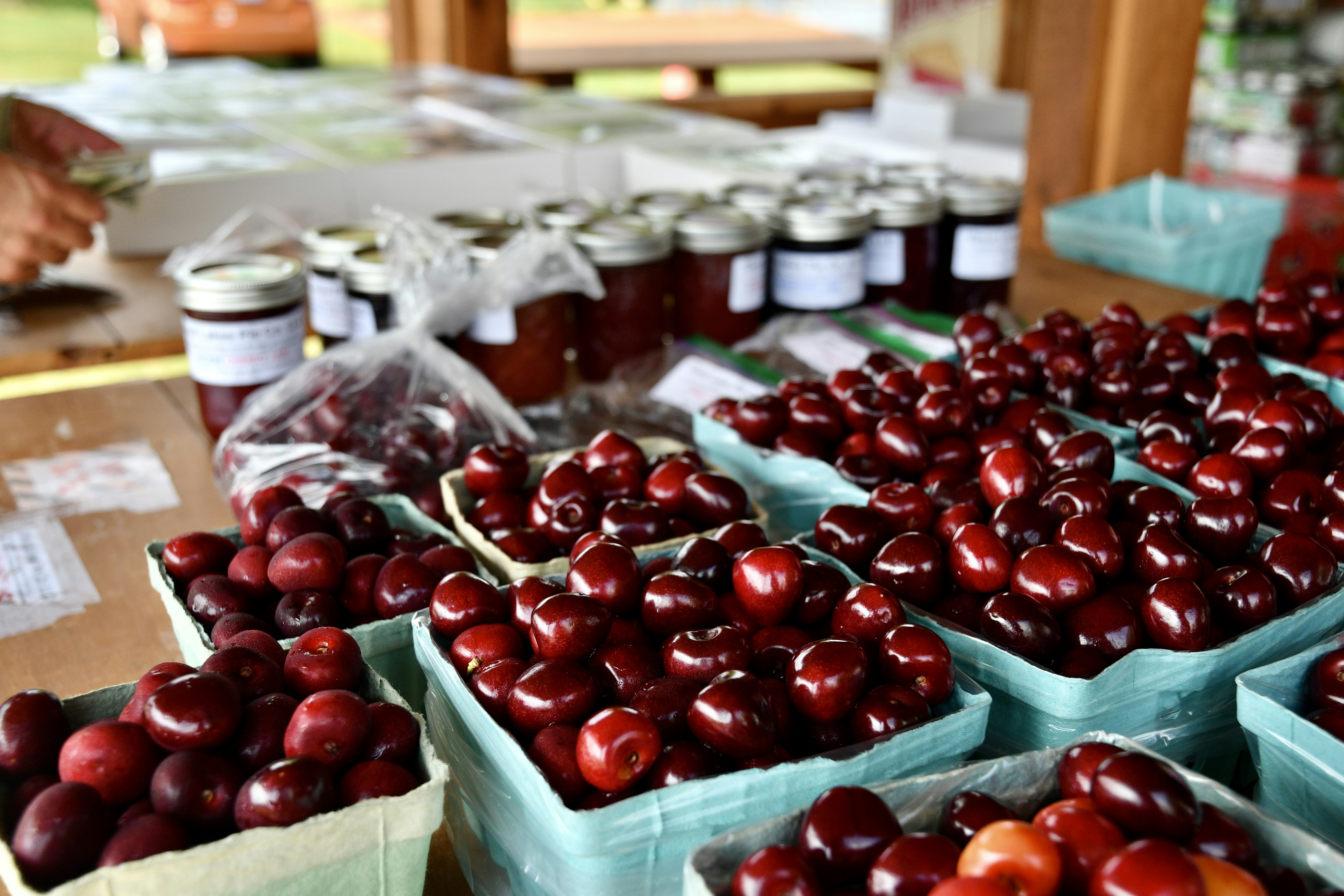 Fresh cherries in green baskets alongside jars of preserves at a market stall.