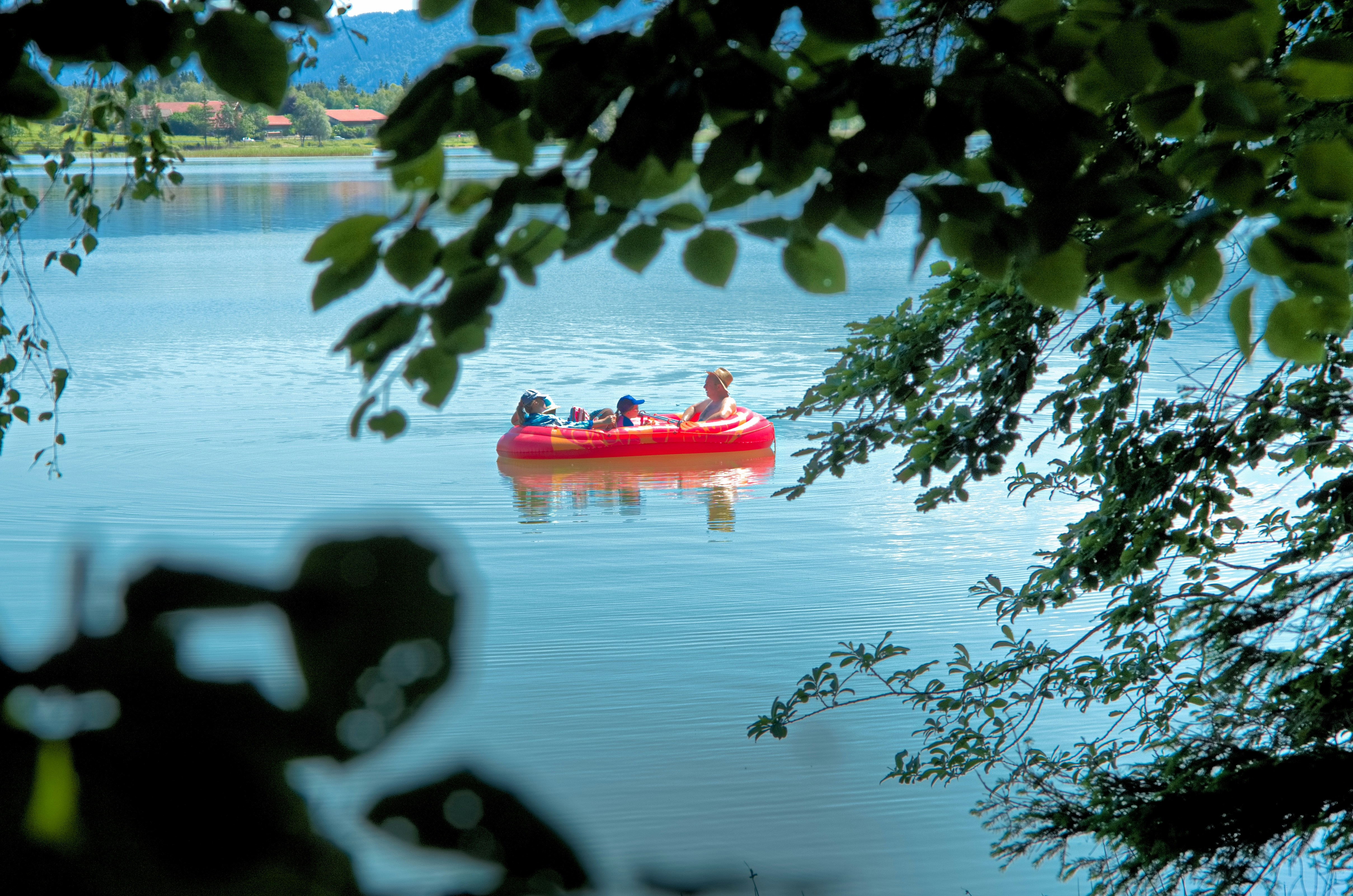 Red kayak glides across a calm lake, framed by lush green leaves.