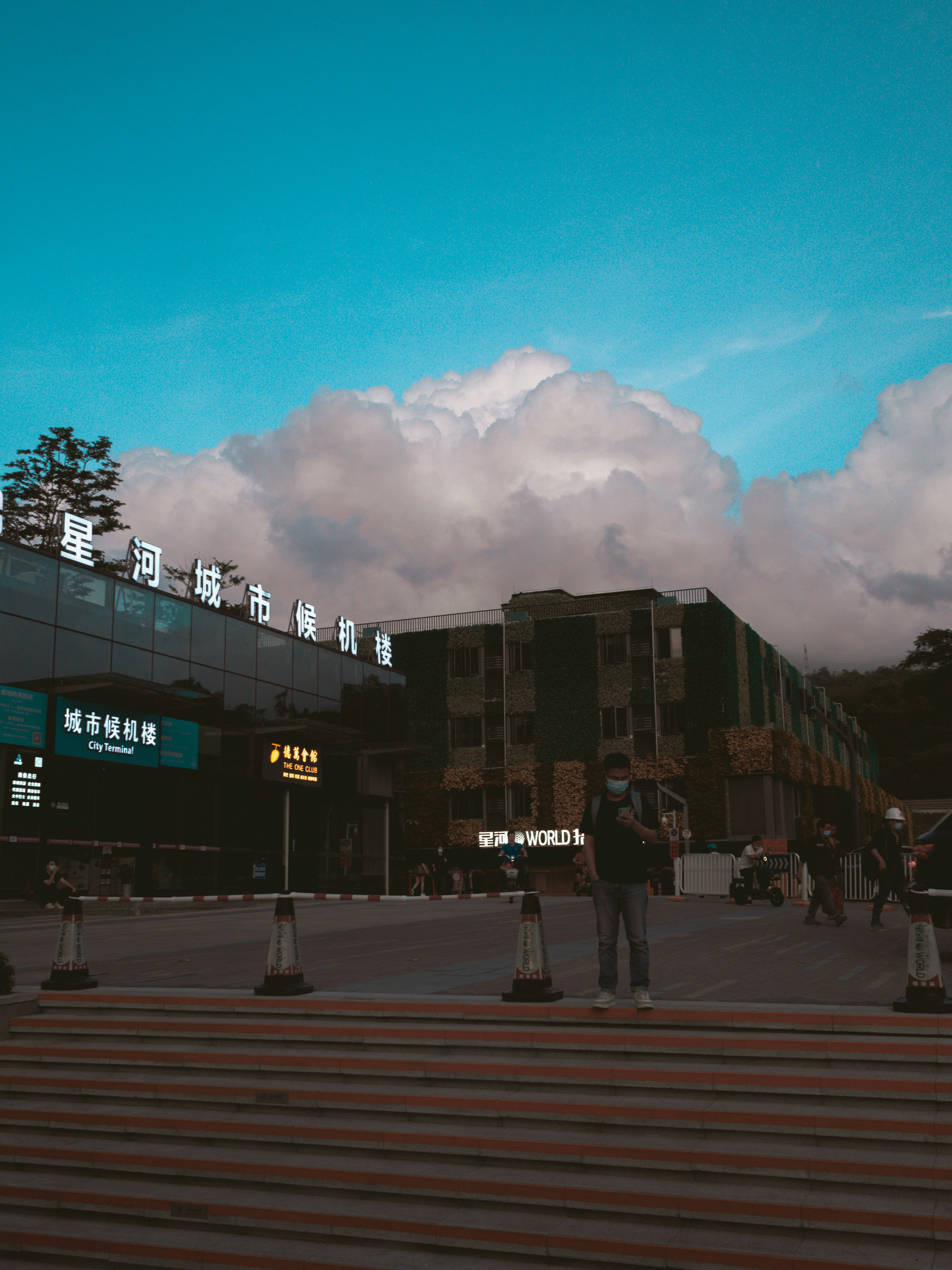 Contemporary building facade with illuminated signage and a pedestrian in the foreground, framed by dramatic clouds and a vibrant blue sky.