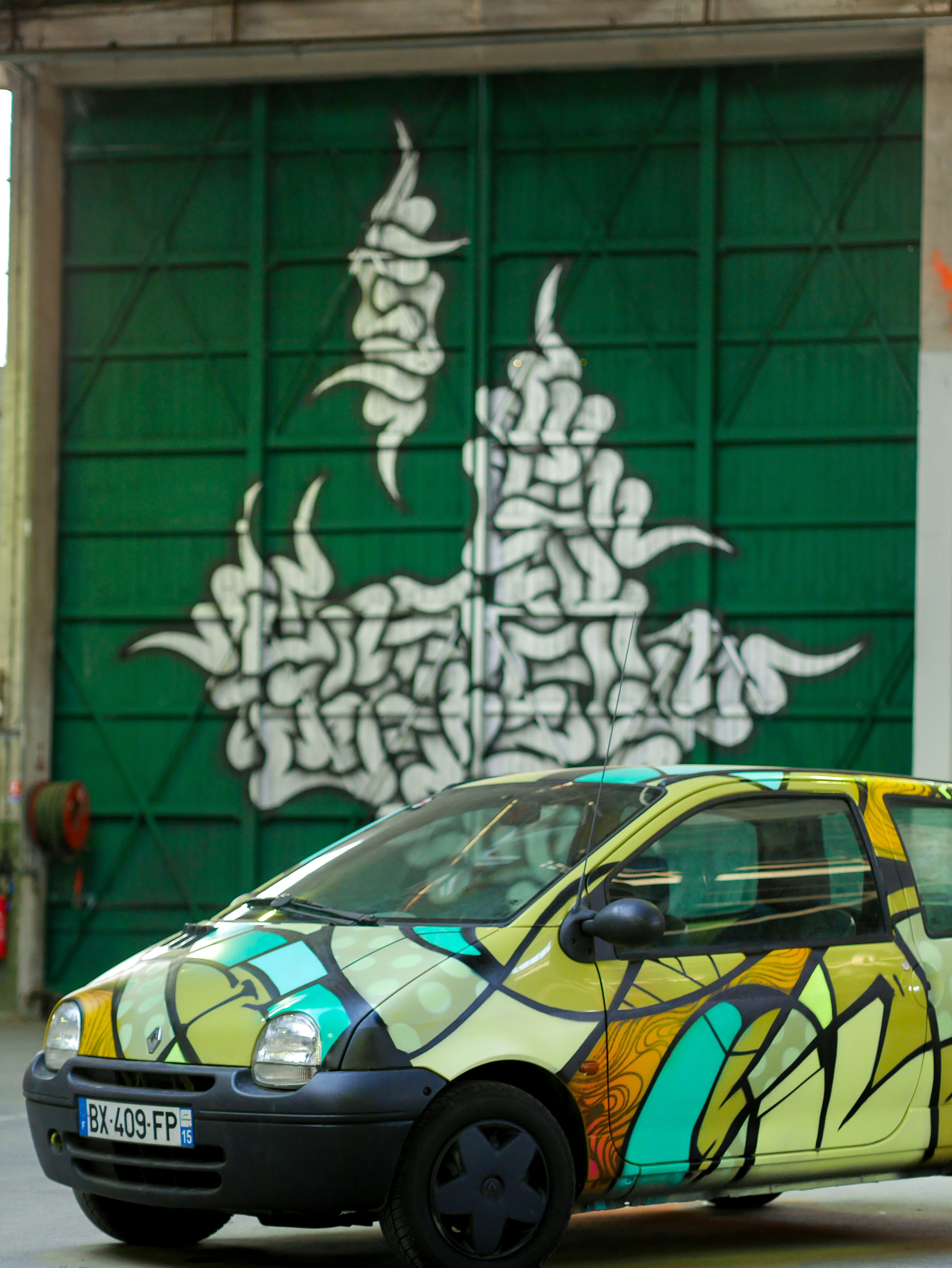 A vibrant, abstractly painted car parked in front of a graffiti-covered garage door, showcasing urban art's dynamic intersection with everyday life.