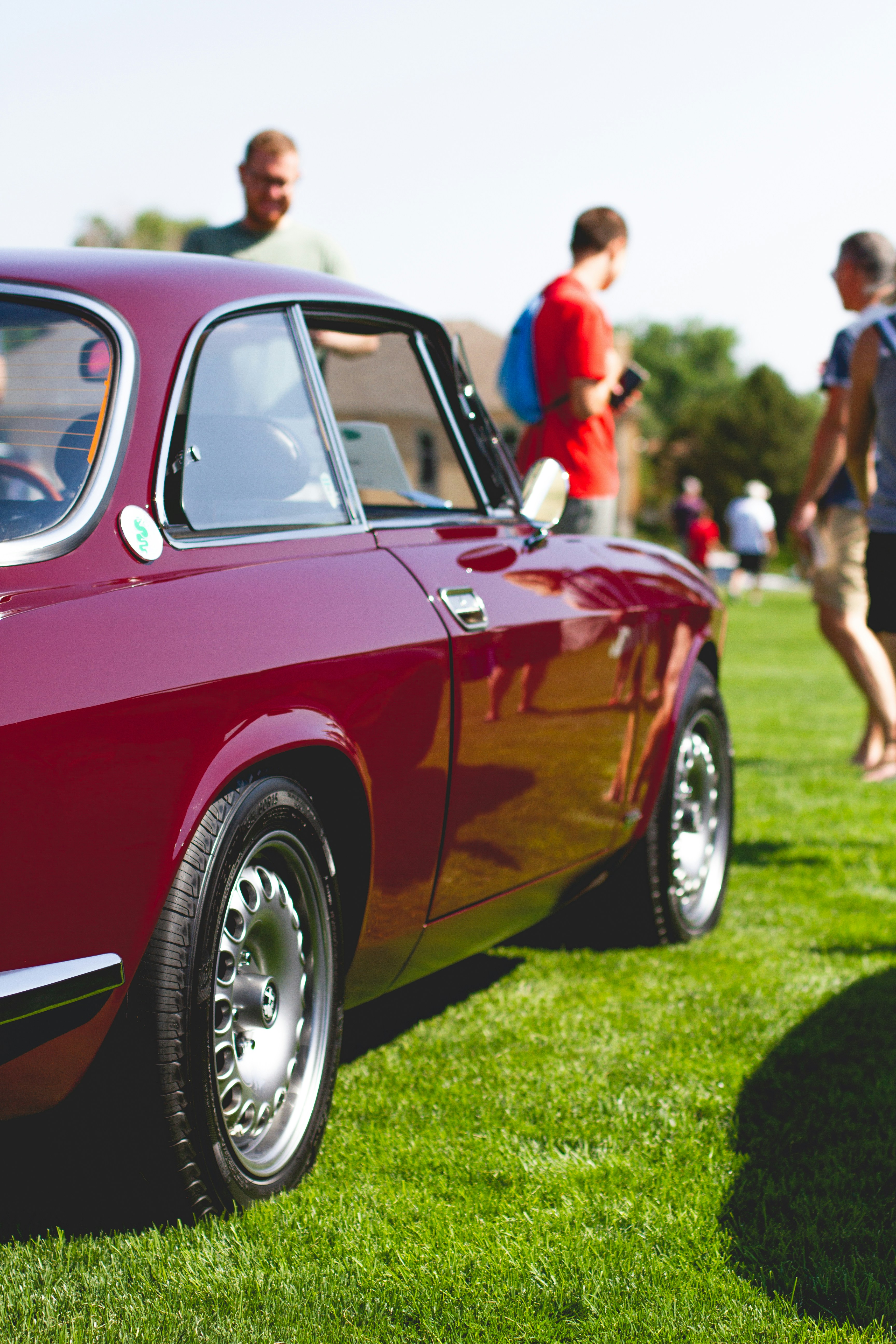 Red vintage car on a green lawn with people in the background.