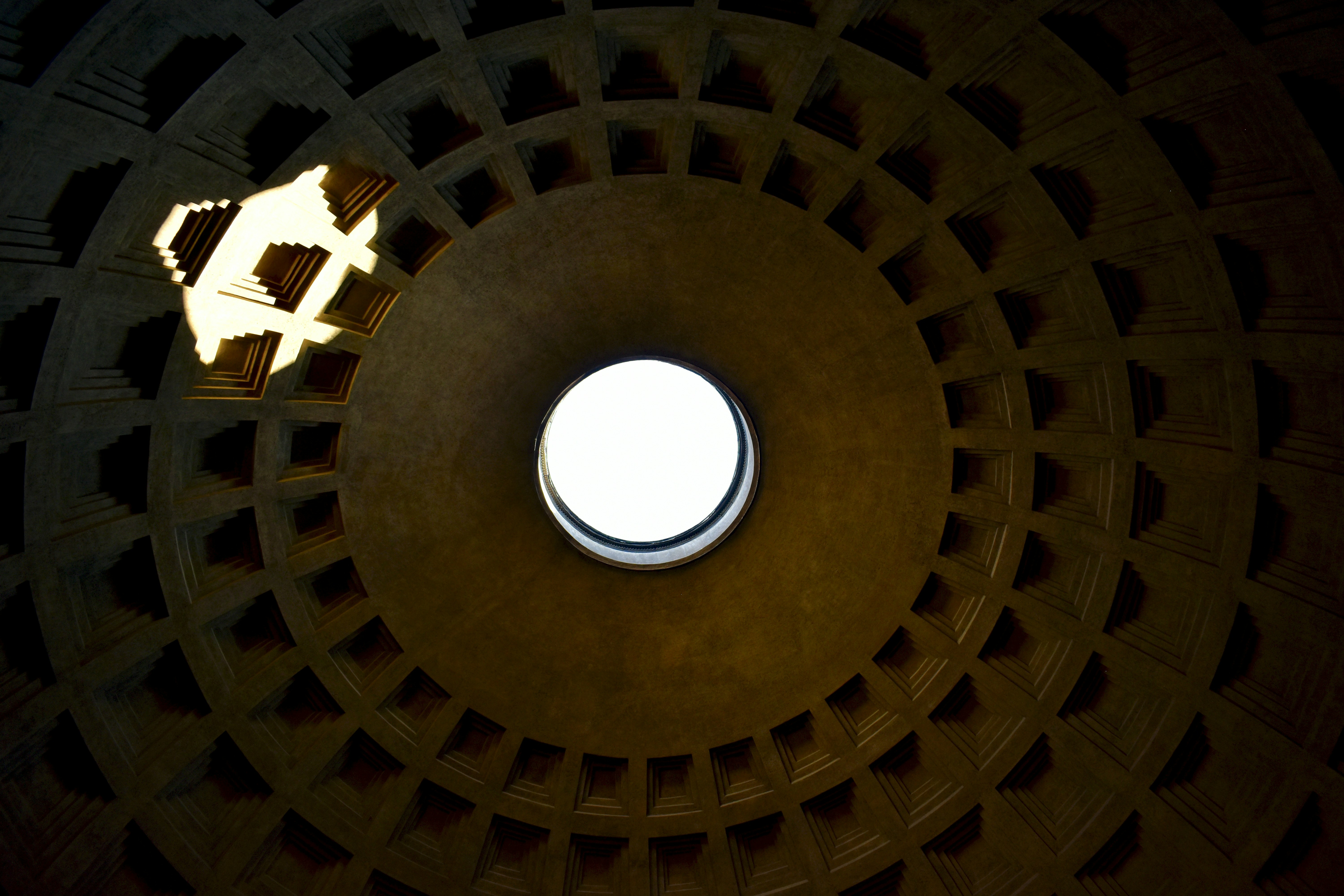Circular ceiling with a central oculus, showcasing intricate patterns and a shaft of light streaming in from above.