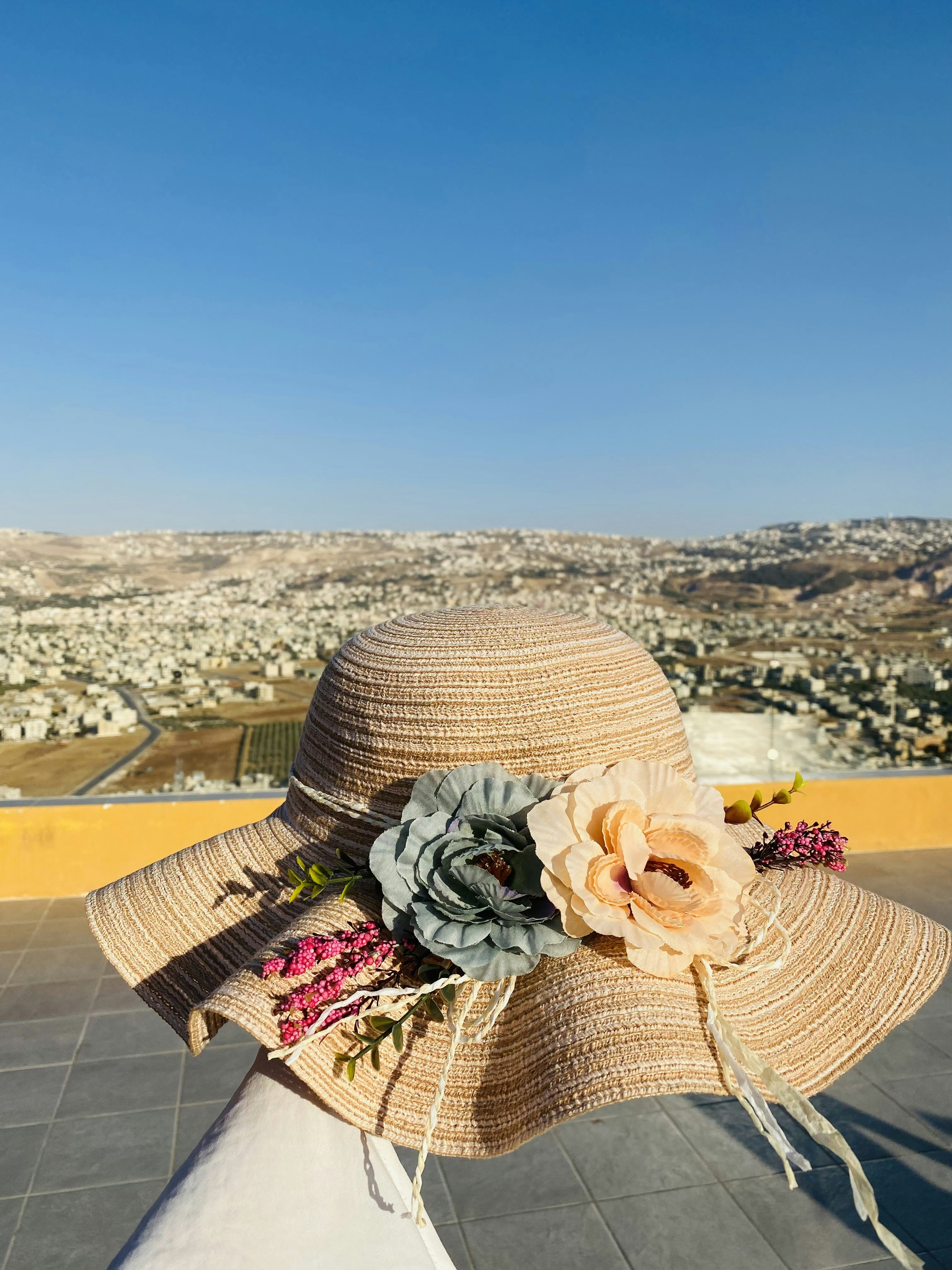 Wide-brimmed straw hat adorned with flowers, overlooking a sprawling landscape under a clear blue sky.
