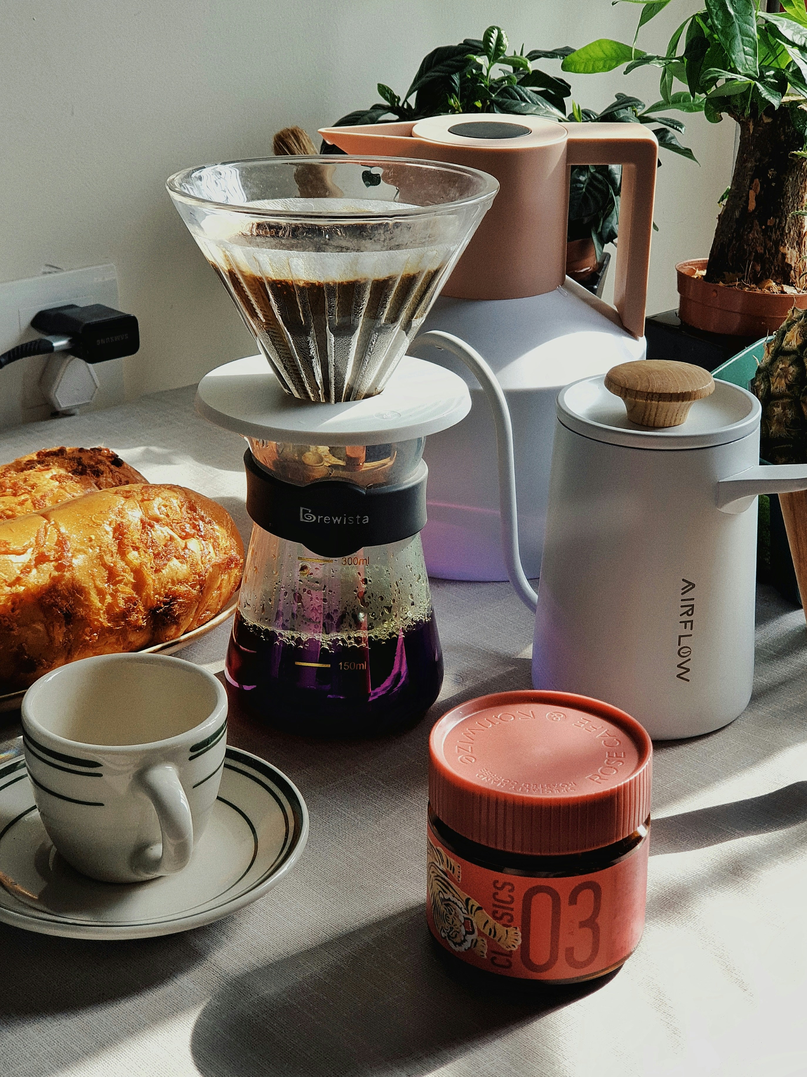 Sunlit Brew Ritual: Glass Dripper Over Purple Carafe with Croissant and Plant
