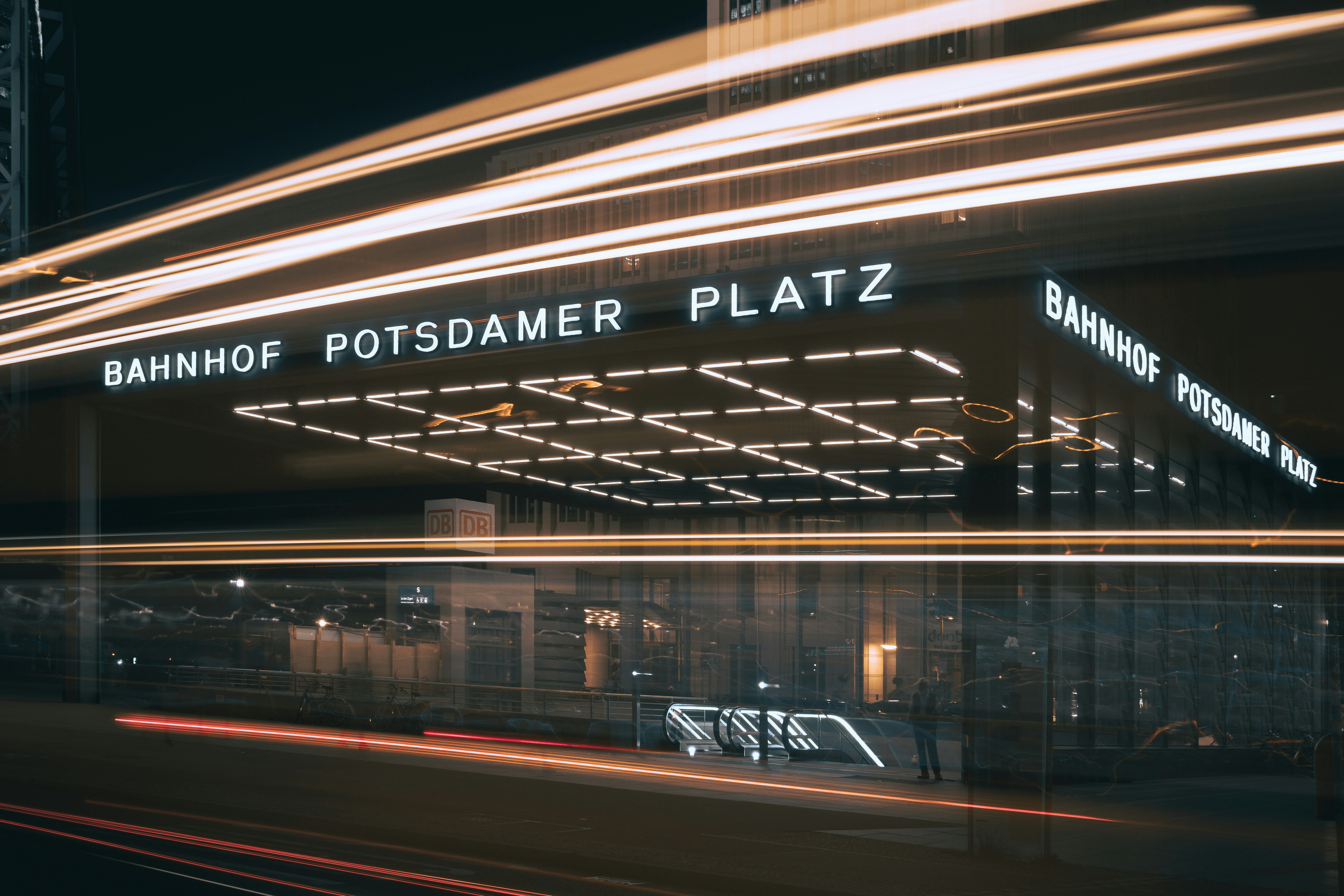 Illuminated sign of Bahnhof Potsdamer Platz reflects the vibrancy of urban nightlife, with light trails capturing the motion of passing vehicles.