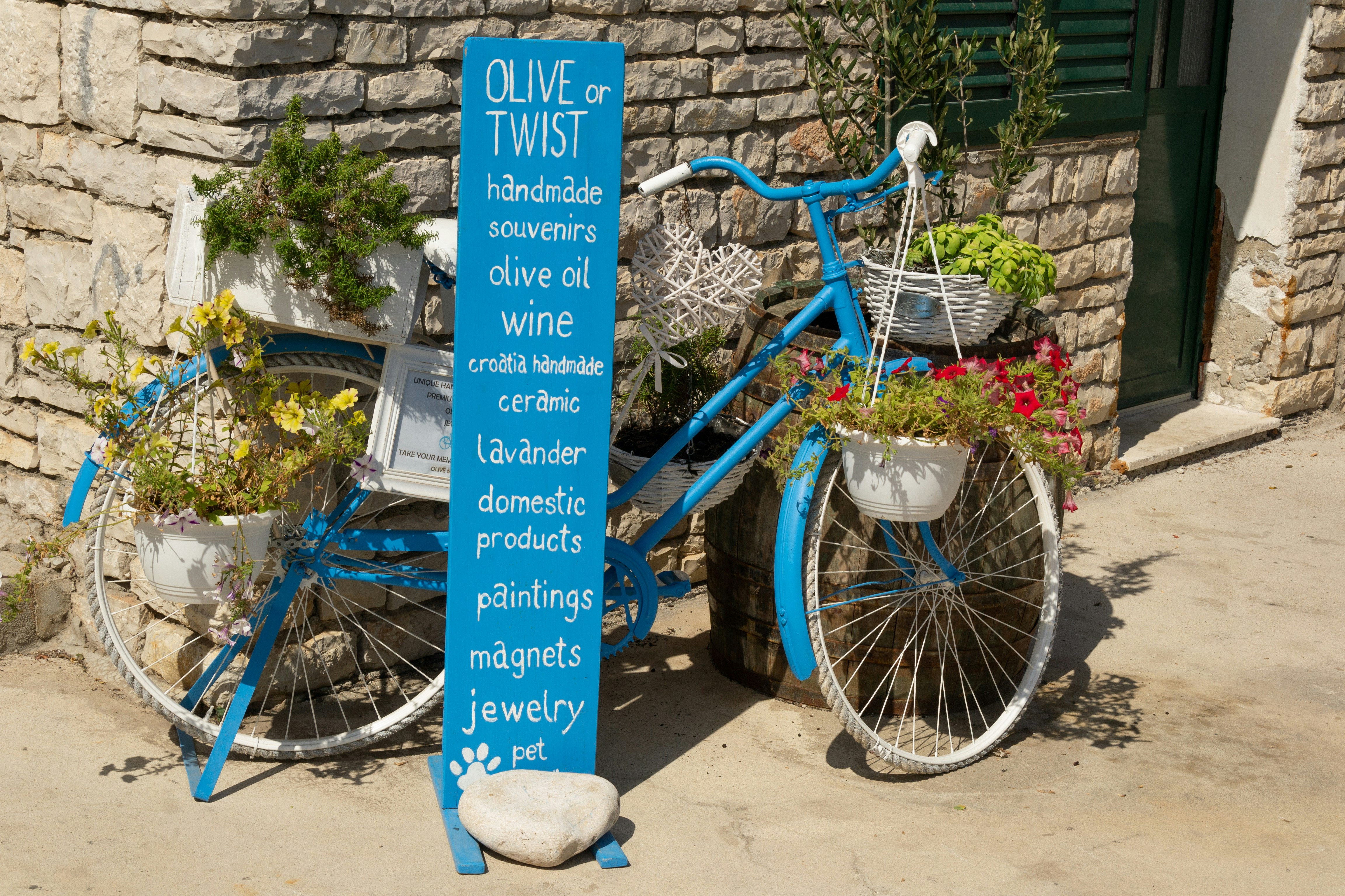 Olive Twist: Blue Signboard Paired with a Mint-Blue Bicycle in Sunlit Courtyard