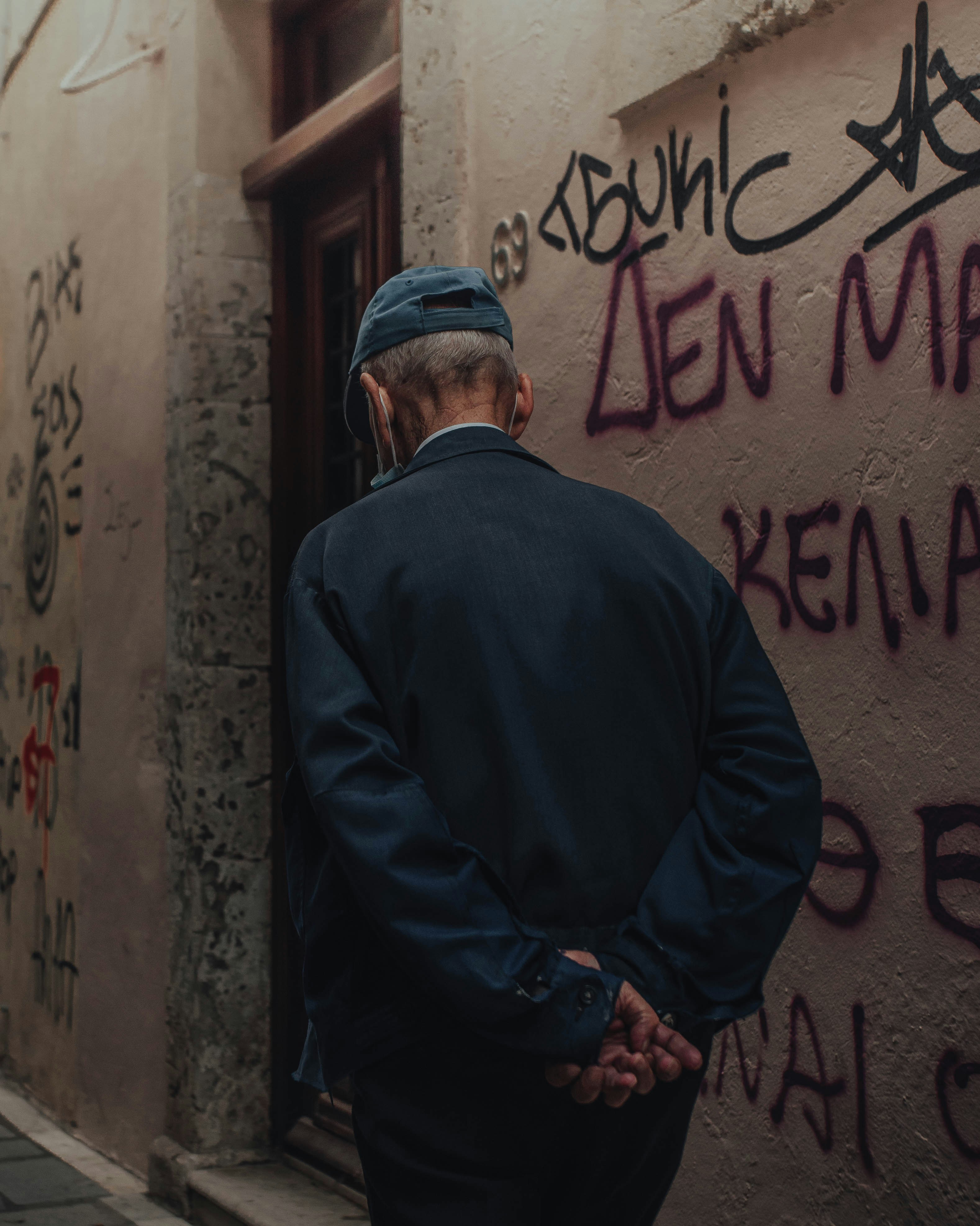 Elderly man walking through a narrow alley adorned with vibrant graffiti, lost in thought.