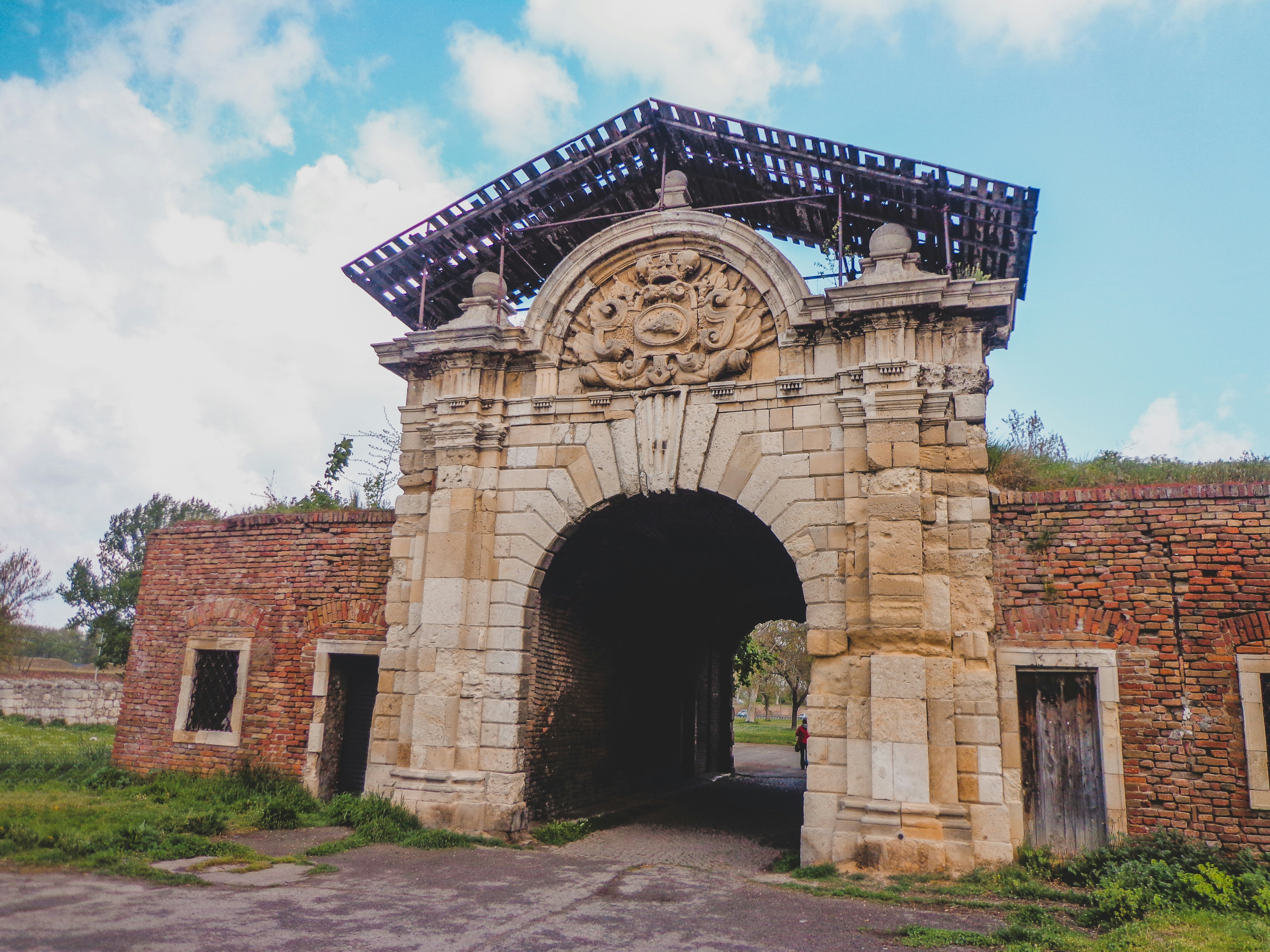 Weathered stone archway framed by red brick walls under a bright blue sky. The gateway stands as the focal point of the ruins.