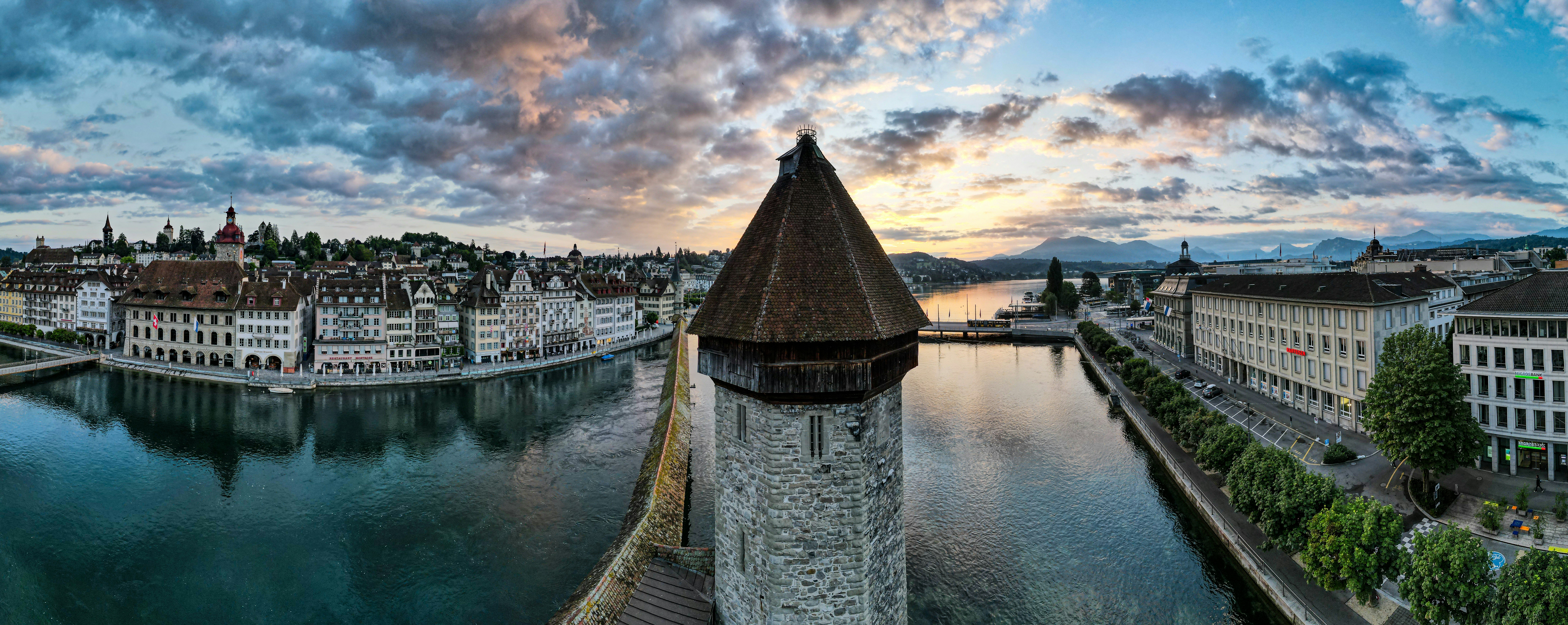 Capture the timeless allure of Lucerne, Switzerland, as dawn breaks over the iconic Wasserturm. This breathtaking panoramic view showcases the historic Chapel Bridge stretching across the emerald waters of the Reuss River. The early morning light paints the sky with a dramatic tapestry of soft pinks and golden ambers, casting a gentle glow over the medieval architecture of the Old Town. Stillness reigns as the city awakens, reflecting a perfect harmony between human heritage and nature’s daily renewal. A serene, evocative tribute to one of Europe’s most storied landmarks.