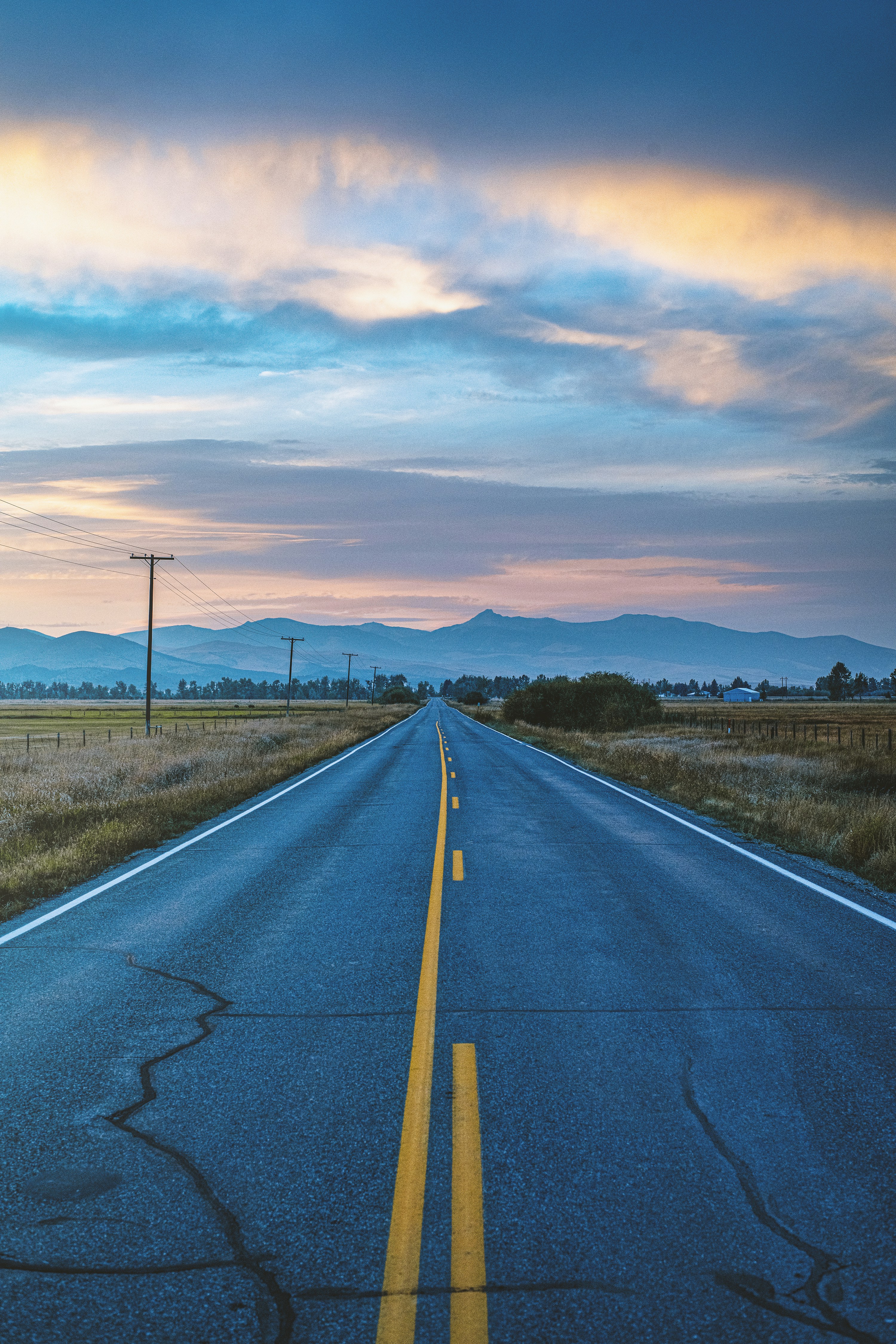 A long, straight road stretches towards distant mountains under a colorful sky at dusk.