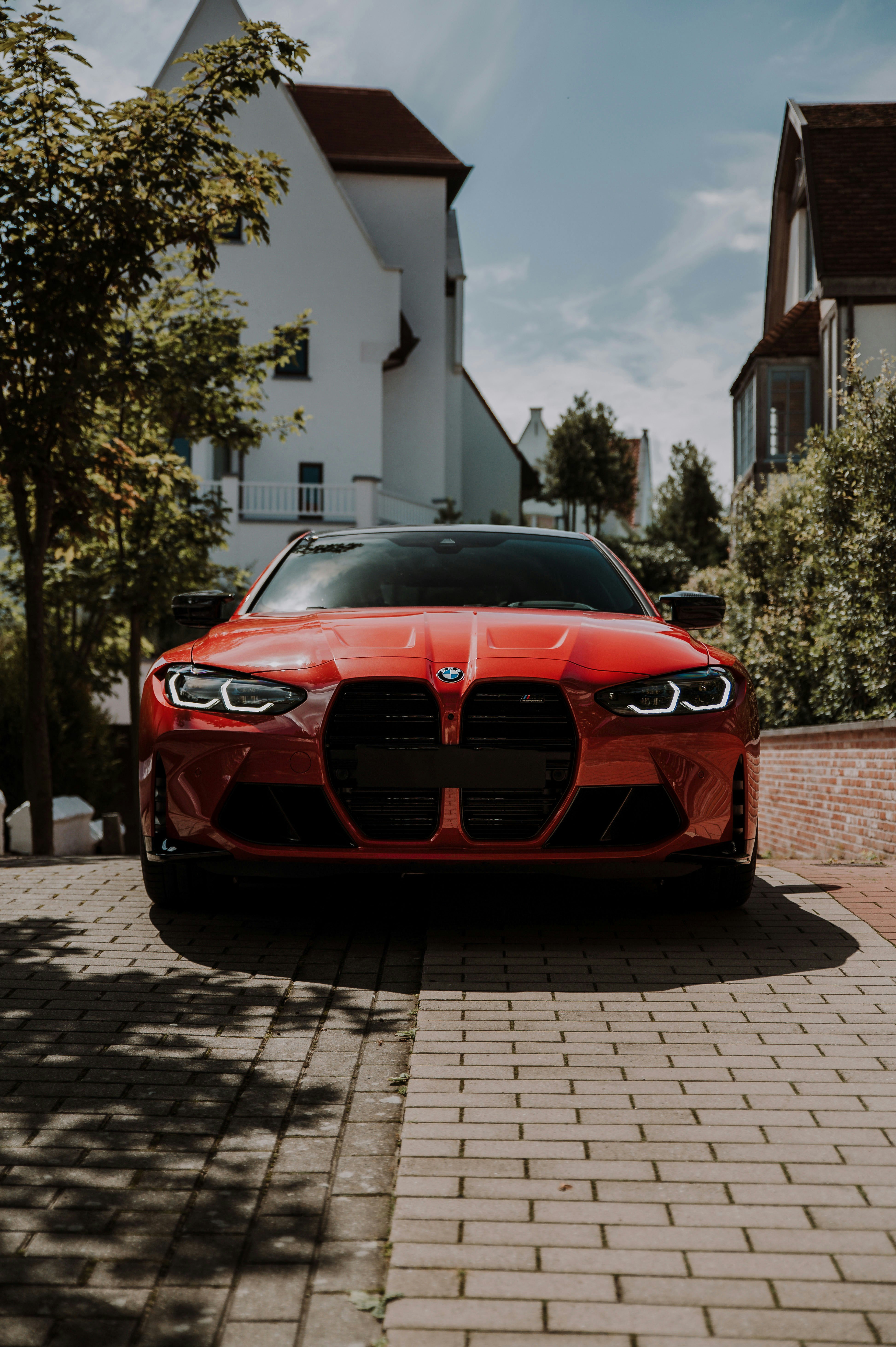 A striking red BMW sports car parked on a cobblestone driveway, surrounded by greenery and modern architecture.