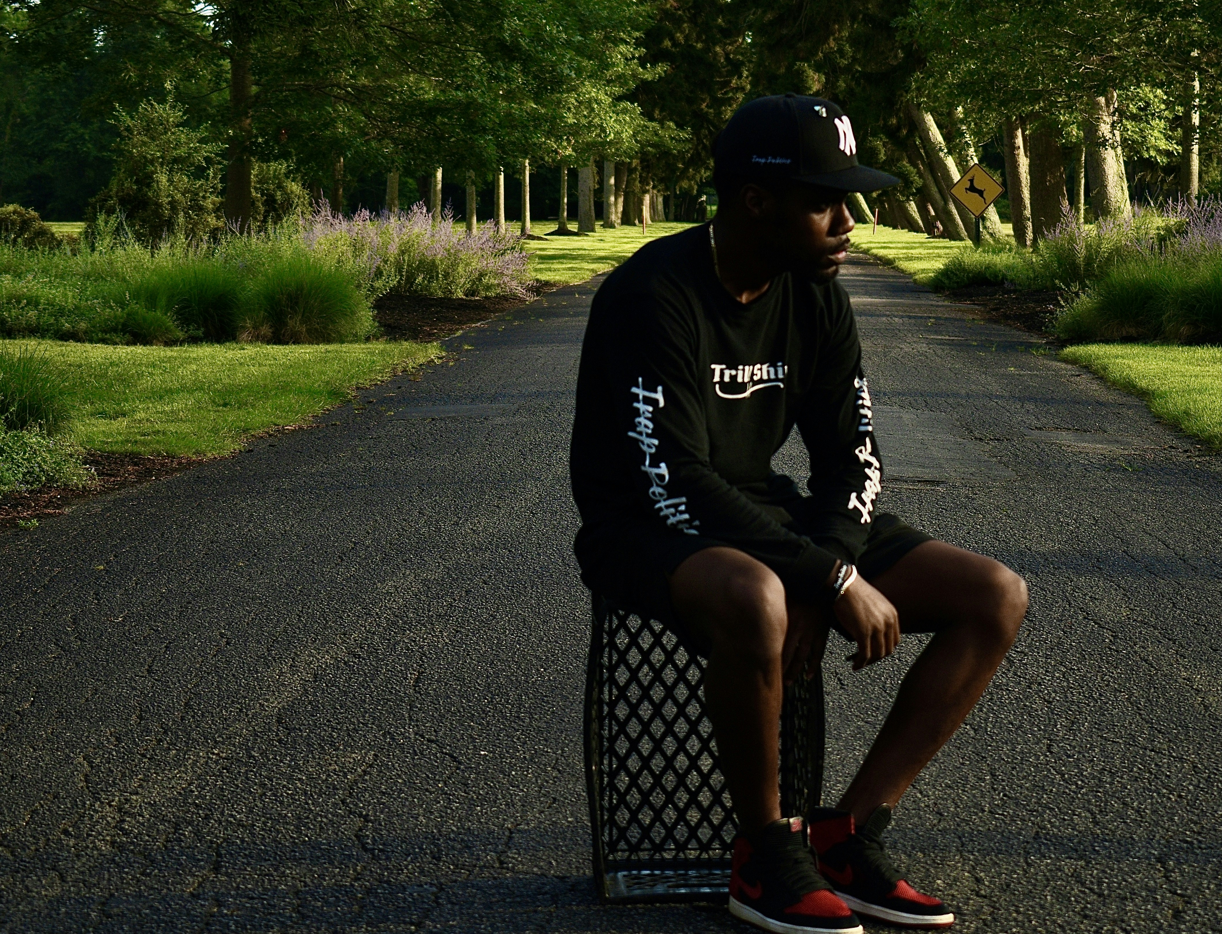 A person seated on a crate along a tree-lined path, embodying a sense of calm amidst nature. The scene captures the interplay of light and shadow.