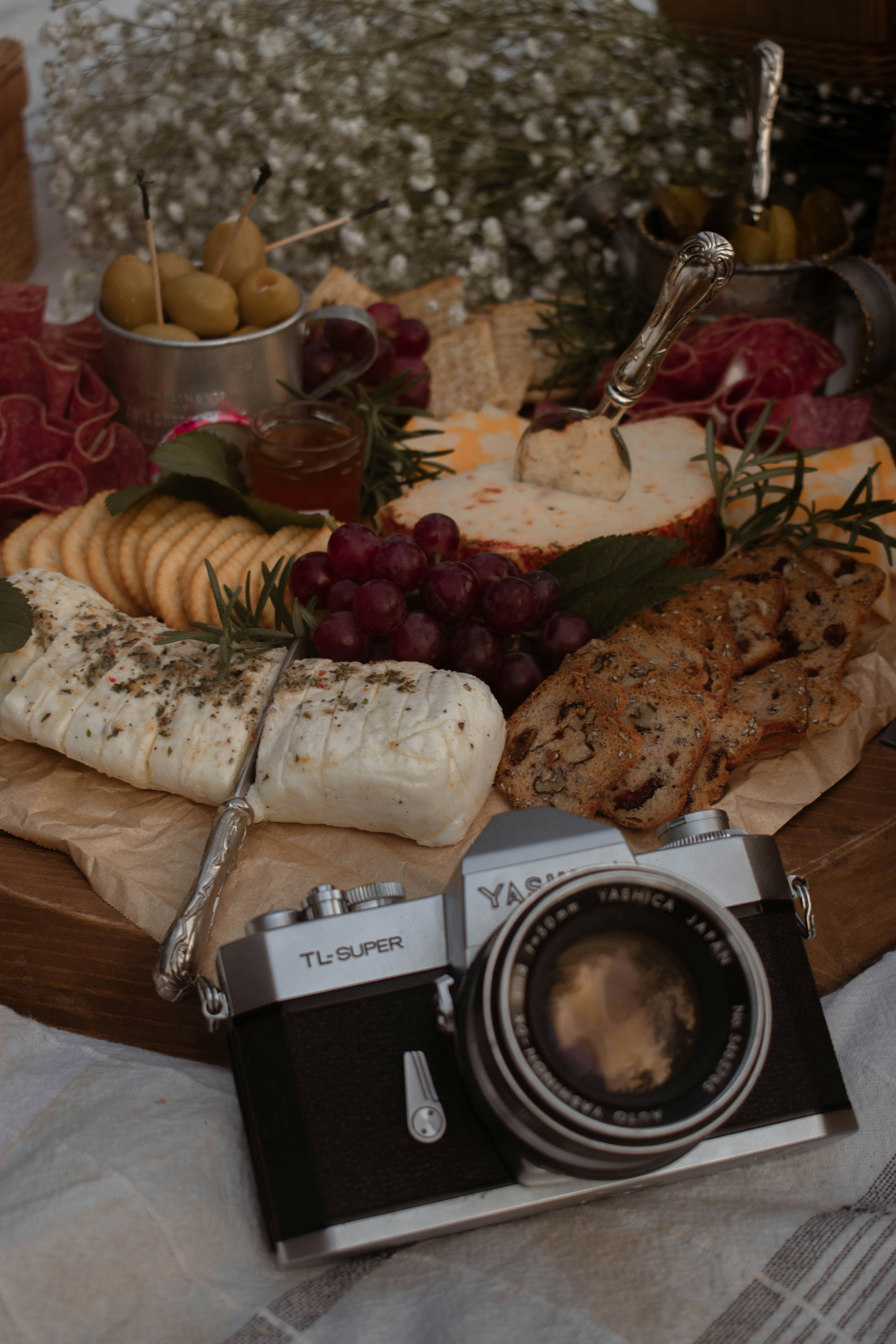 An elegant charcuterie board featuring an assortment of cheeses, meats, and fruits, complemented by a vintage camera in the foreground.