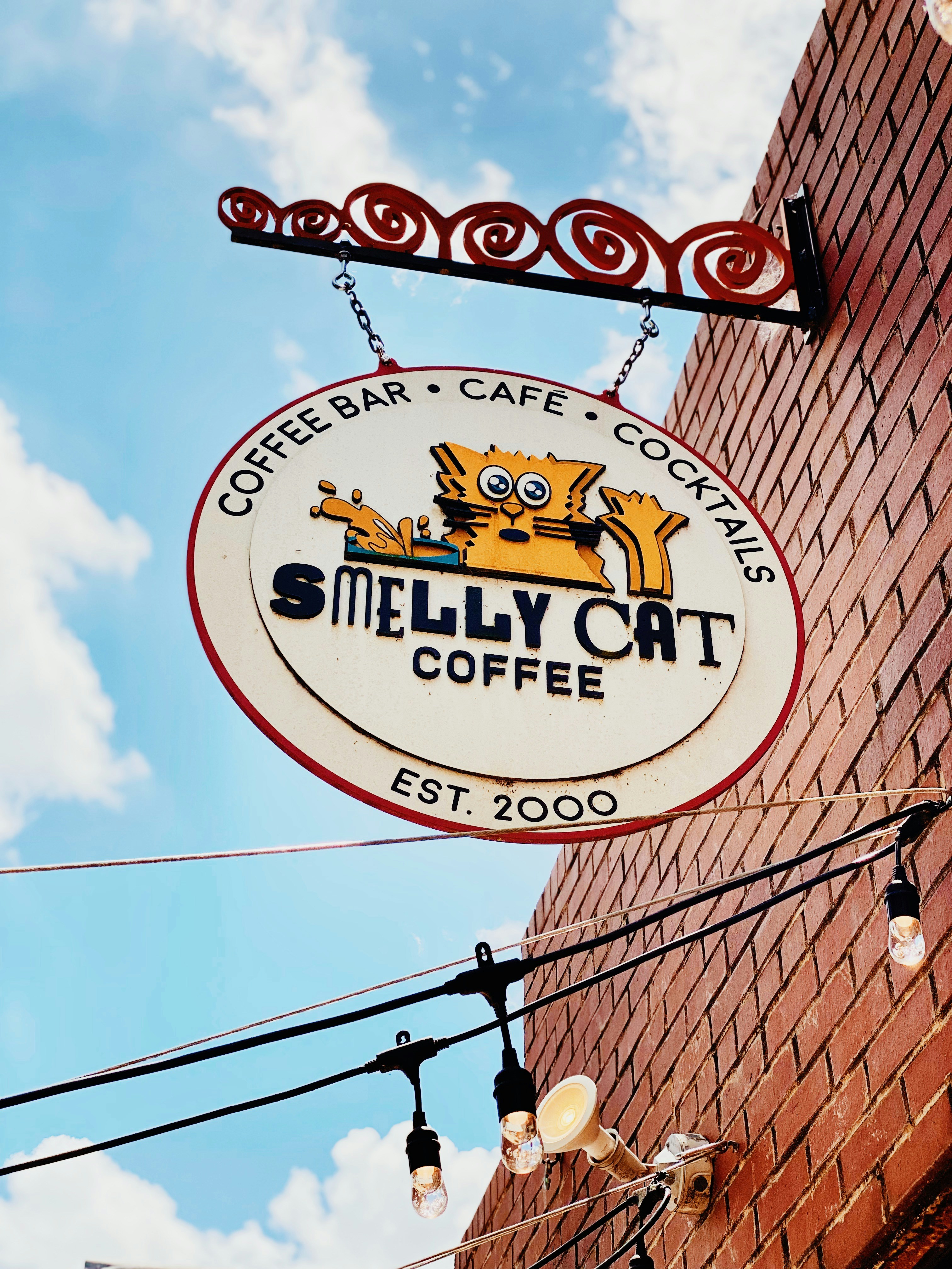 Sign for Smelly Cat Coffee, featuring a playful cartoon cat holding a coffee cup. Established in 2000, it invites patrons to enjoy coffee, cocktails, and a cozy atmosphere.