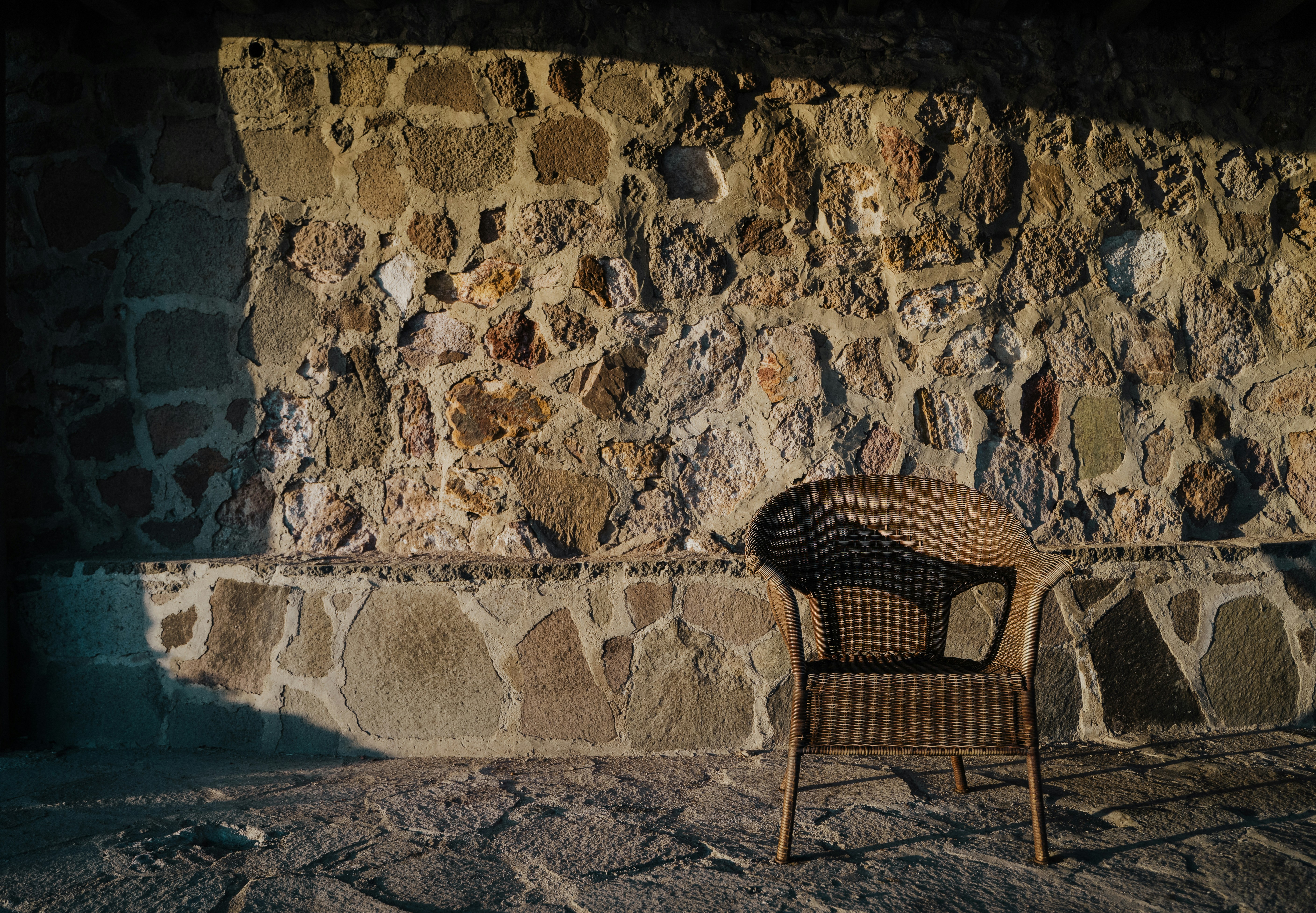 Solitary Wicker Chair Under Dusk Light Against a Rugged Stone Wall