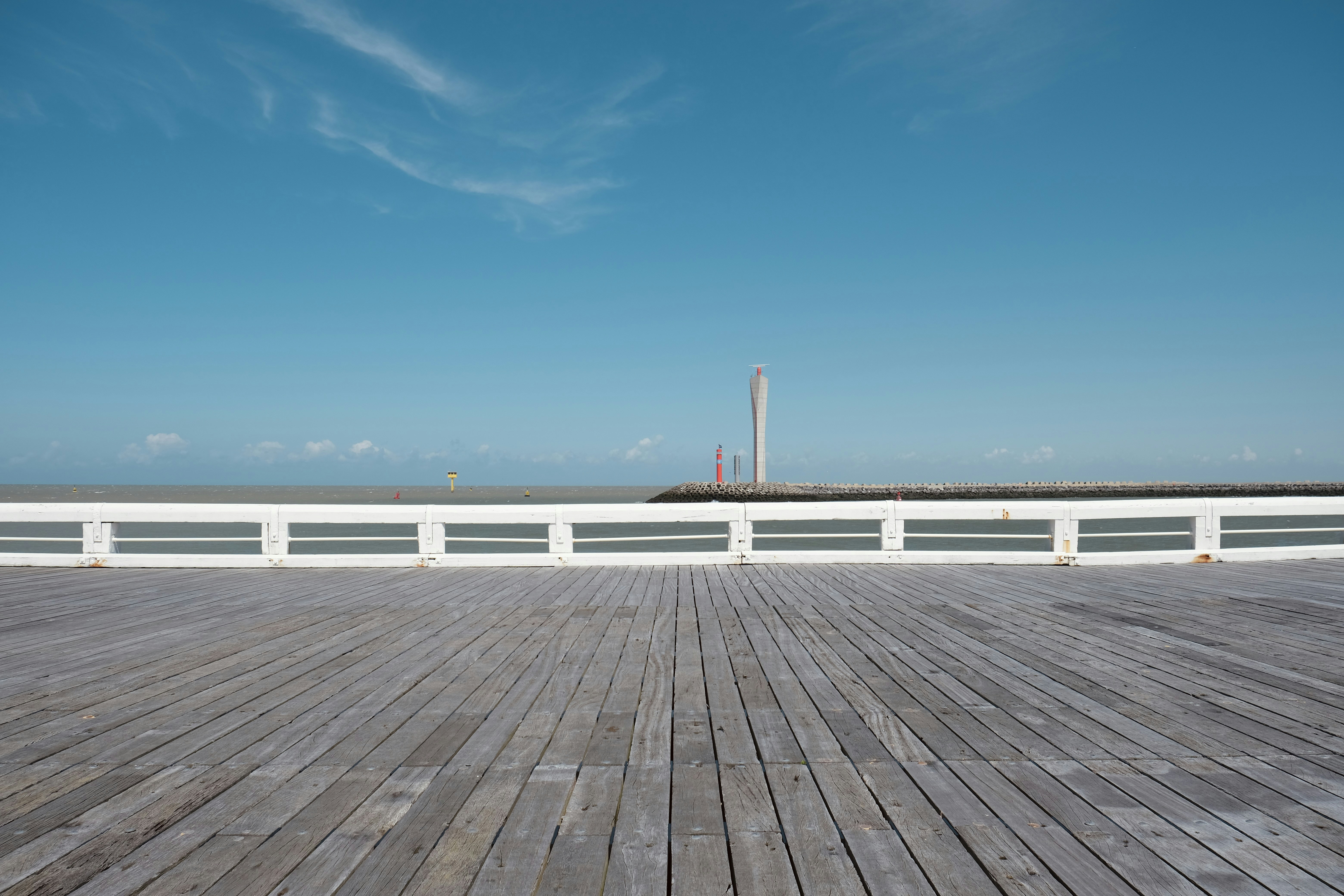 White wooden dock stretching into the blue sea under a clear sky.