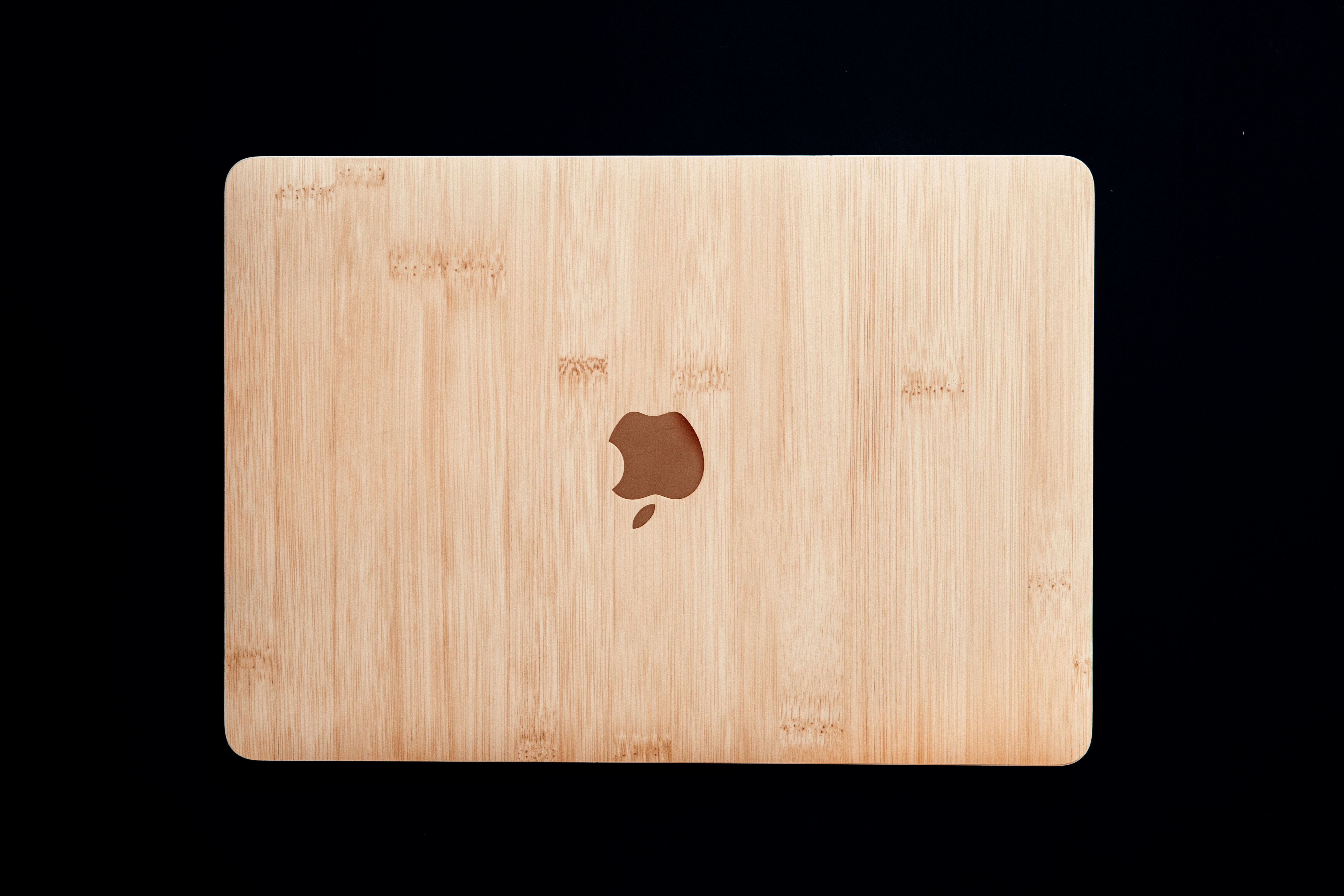 A sleek bamboo MacBook top view showcasing its elegant design and iconic logo against a dark background.